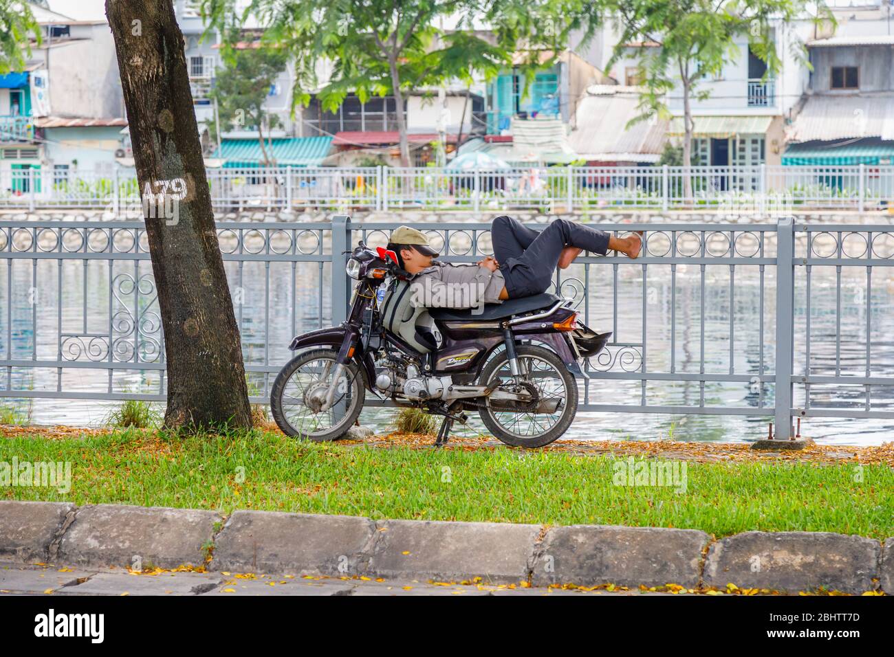 A local man rests sleeping on his Honda Super Dream motorbike by a ...