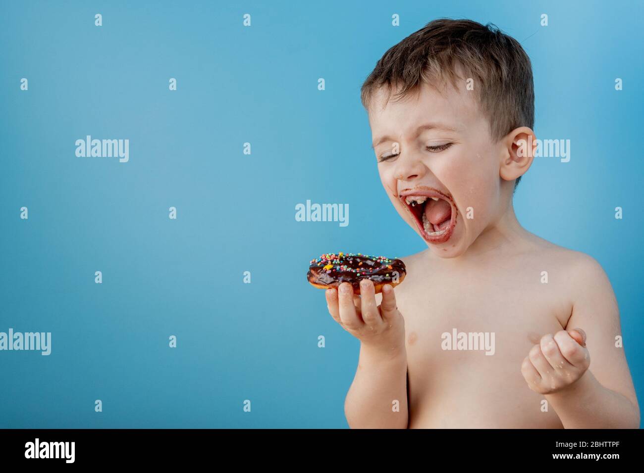 Little boy eating donut chocolate on blue background. Cute happy boy ...