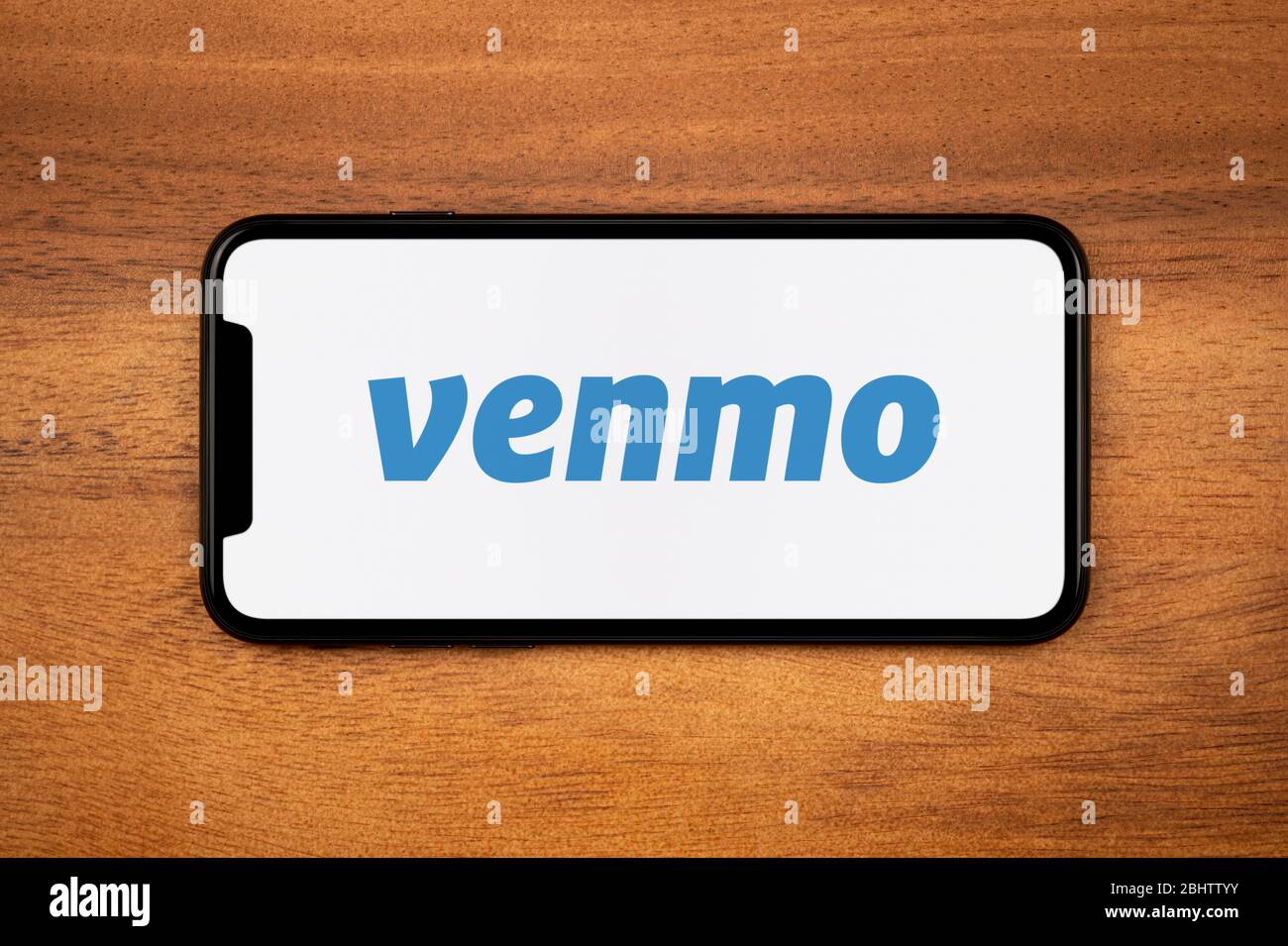 A smartphone showing the Venmo logo rests on a plain wooden table ...
