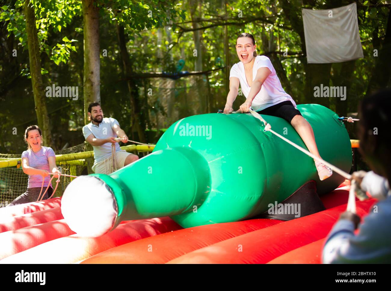 Smiling adults having fun in outdoor amusement park, pulling ropes of ...