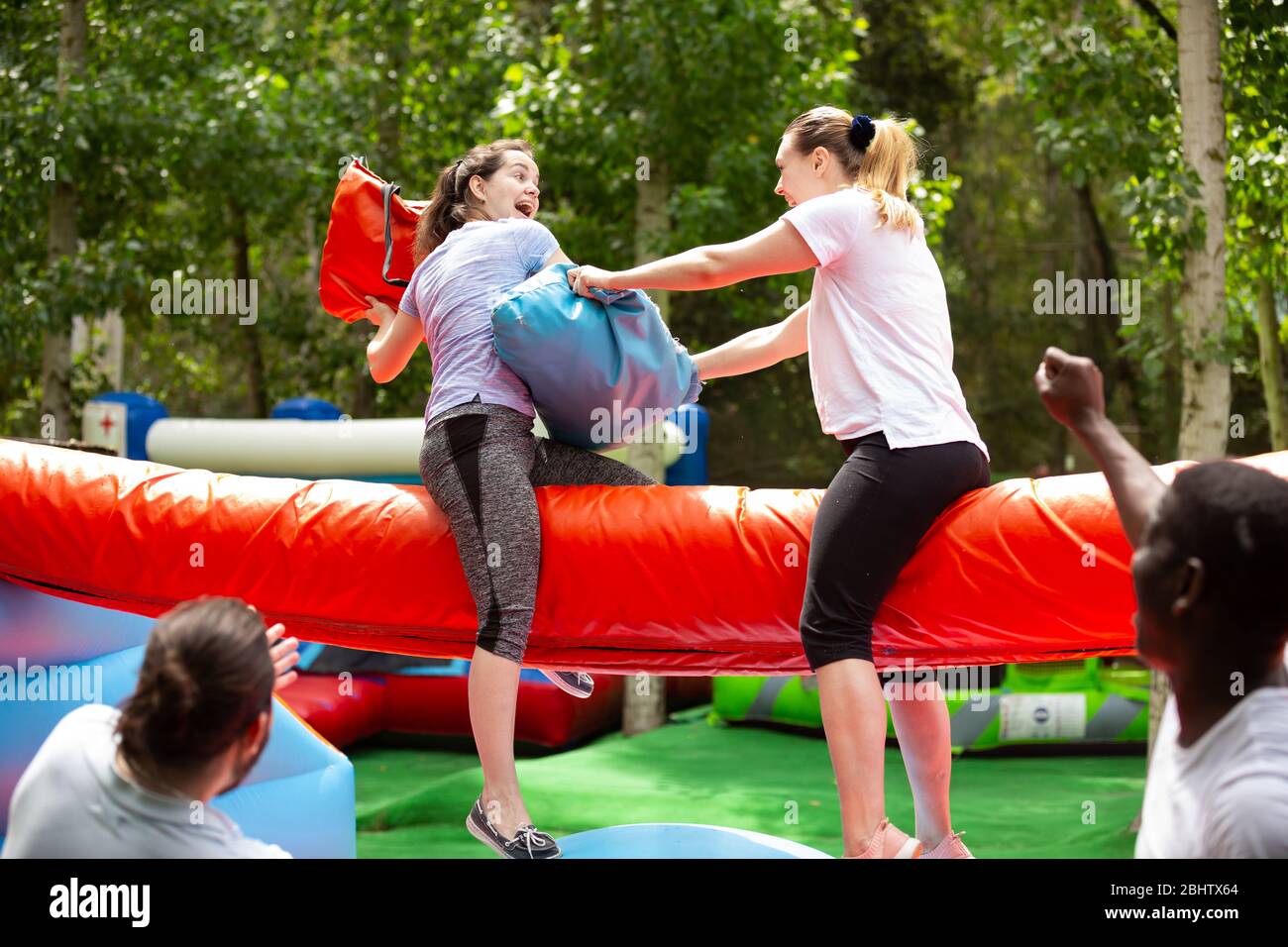 Laughing woman fighting by pillows with her female friend while sitting ...