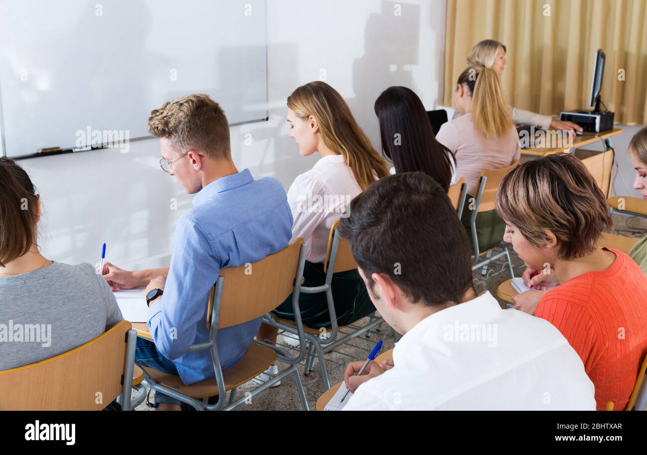 Passing exam. Concentrated adult students working in classroom with ...
