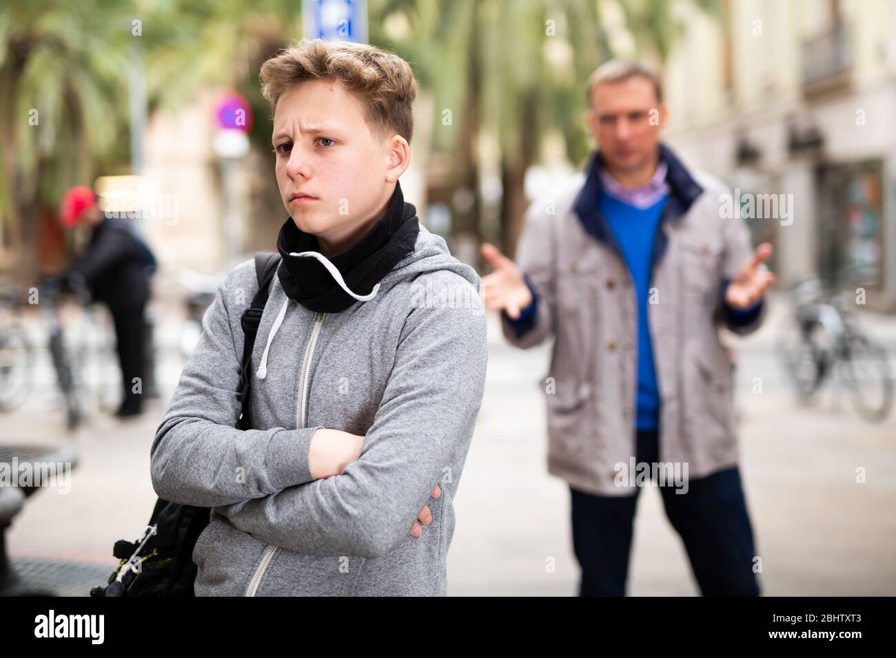 Frowning teenager listening to reprimanding from his father on city ...