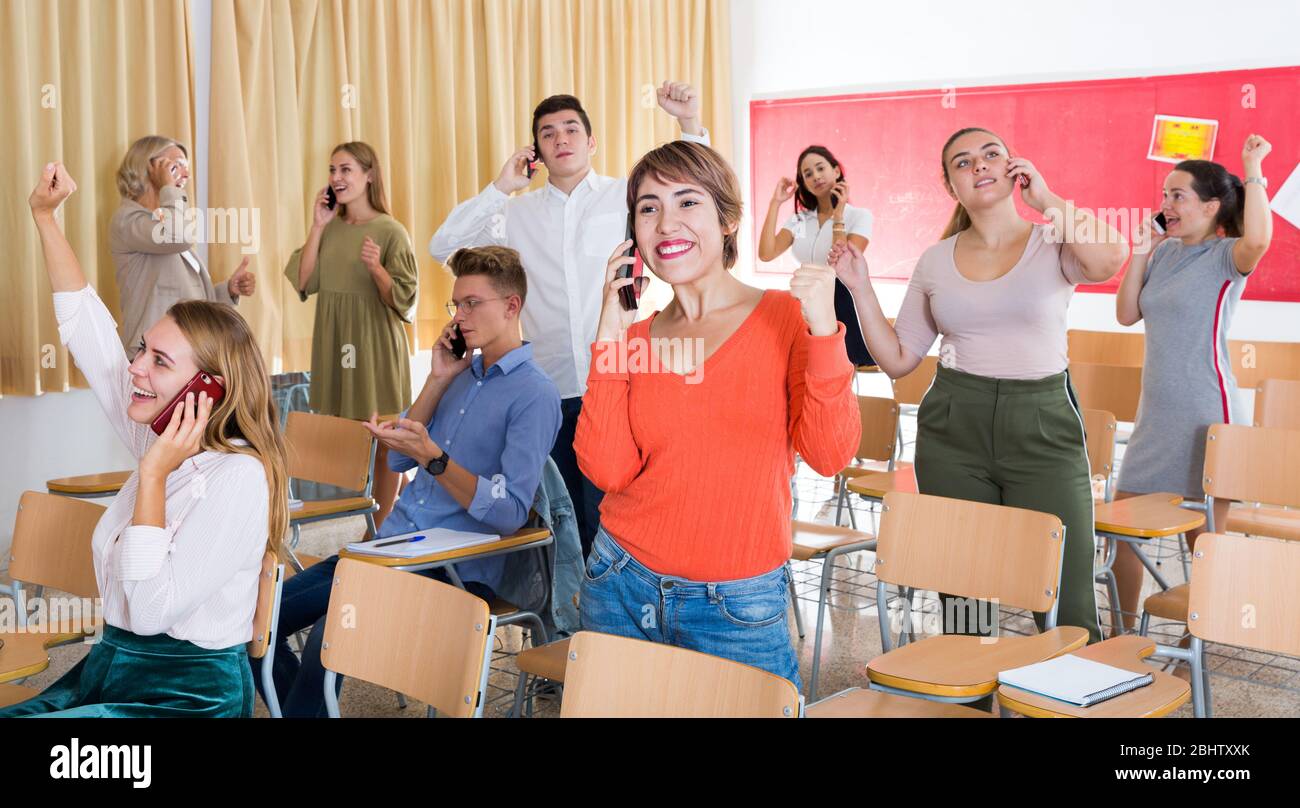 Excited student group talking on phones in classroom while having break ...