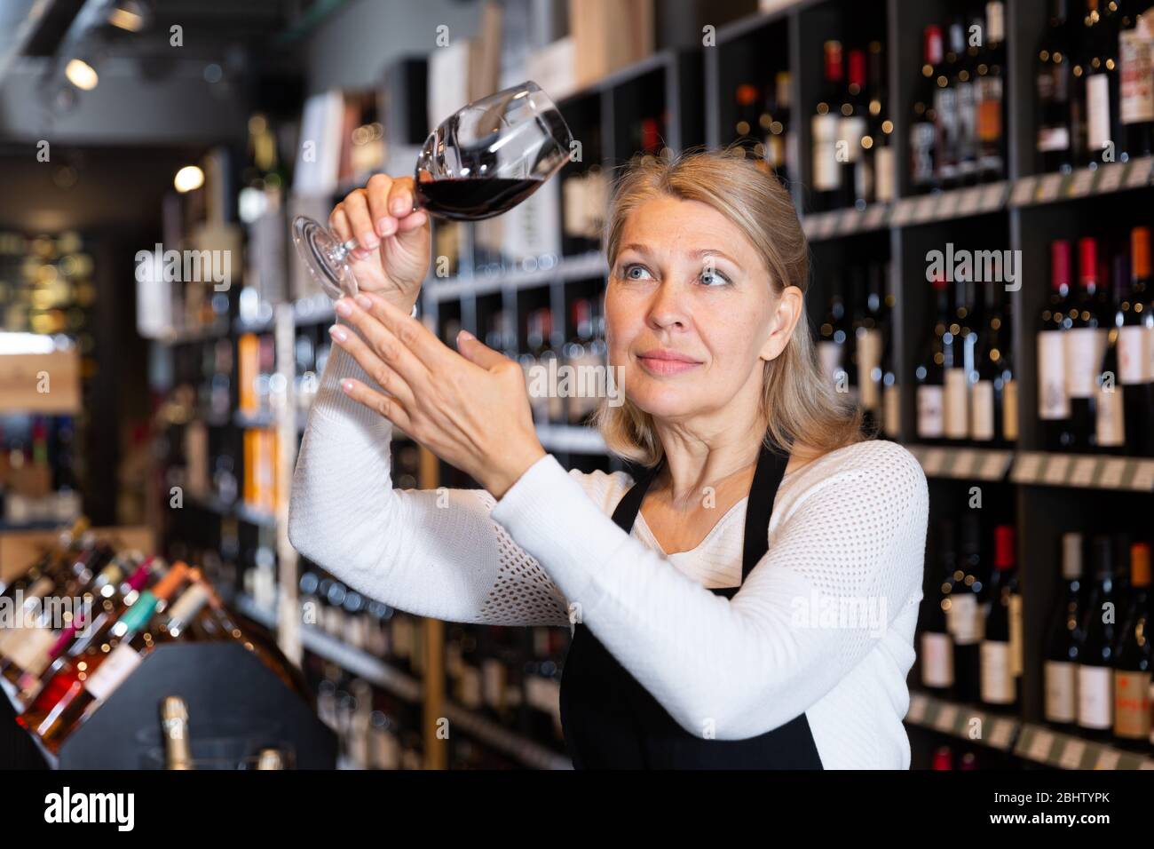 Portrait of middle aged woman professional sommelier tasting natural ...