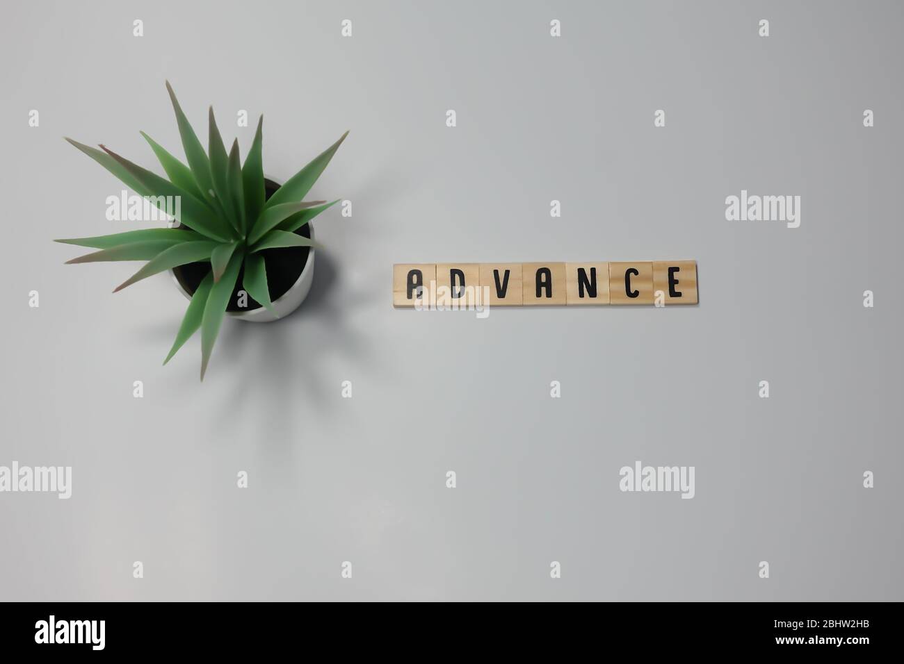 The word Advance is written in wooden letter tiles on a white ...
