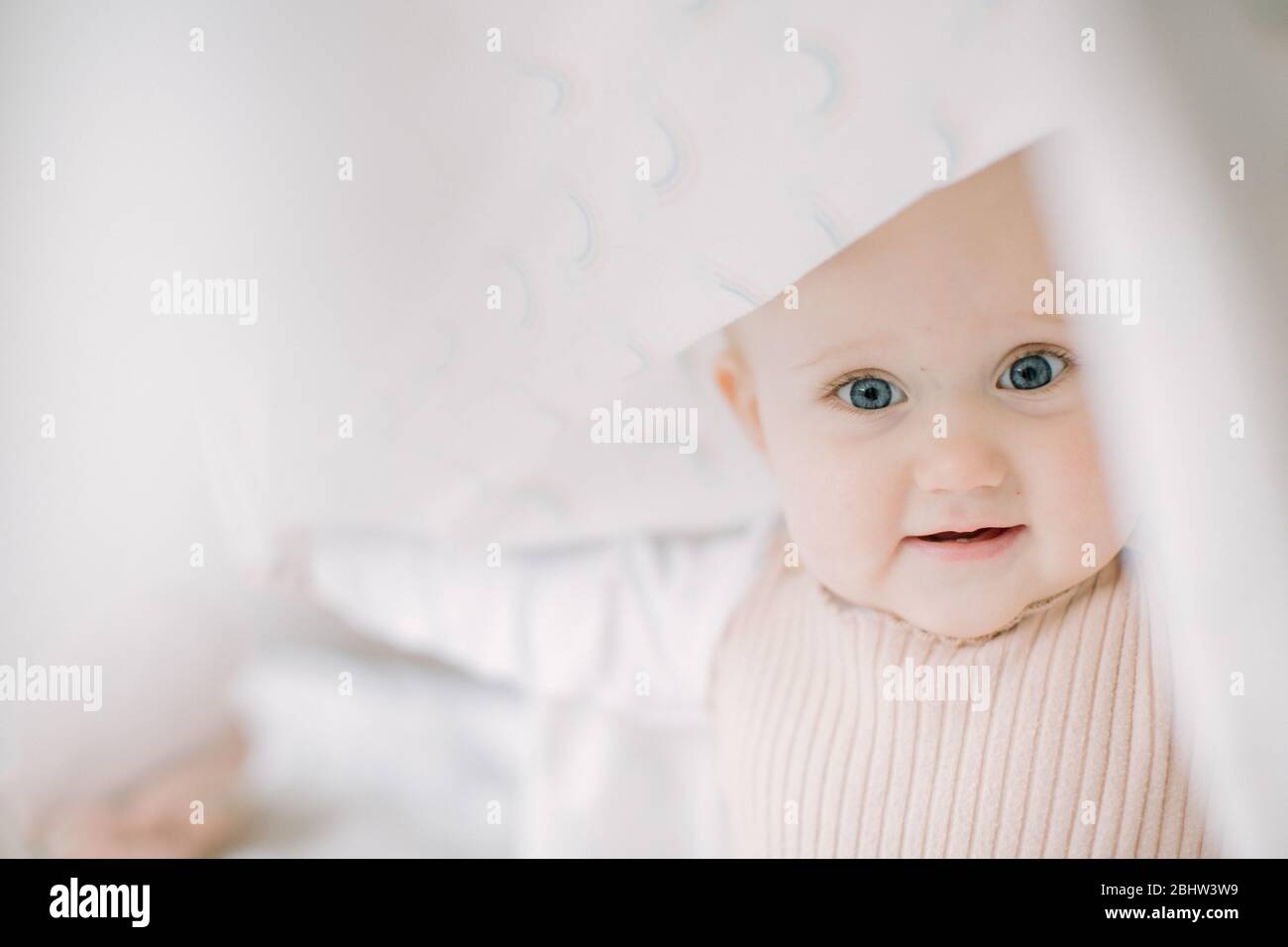 Baby girl looking at the camera while playing under a blanket Stock ...