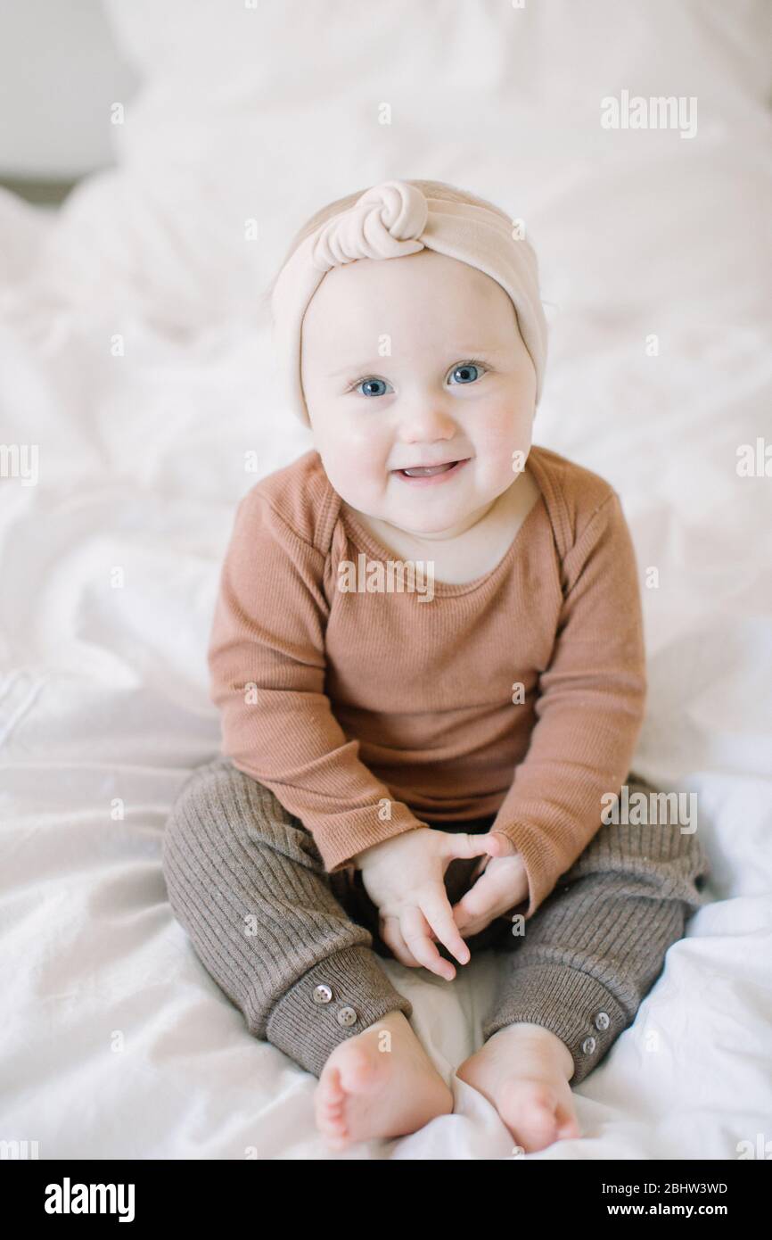Baby girl sitting up on bed and smiling at camera Stock Photo - Alamy