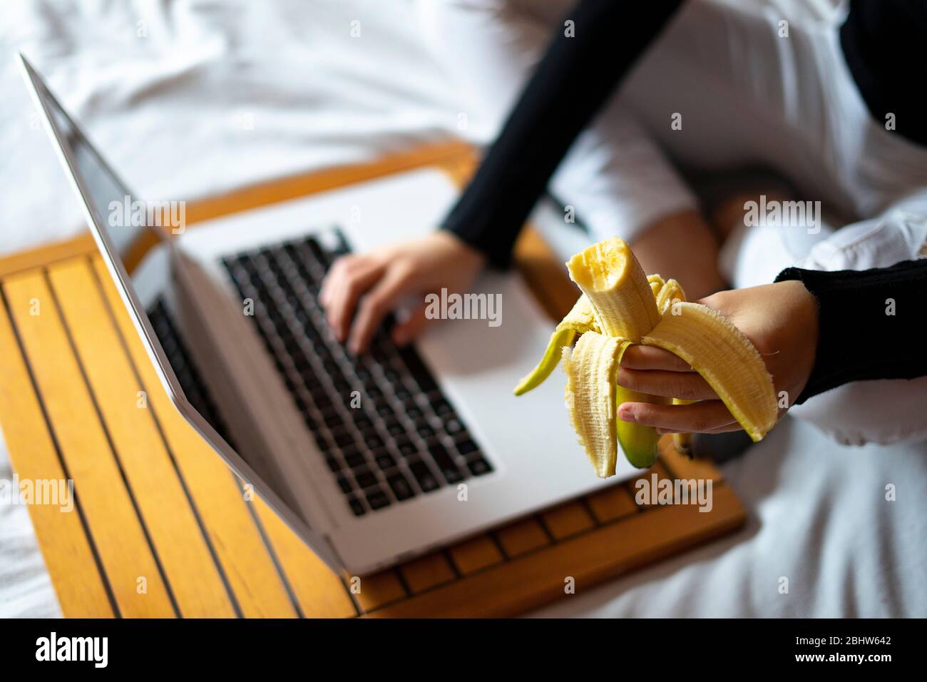 Woman working in bed with the computer and eating a banana. work and ...