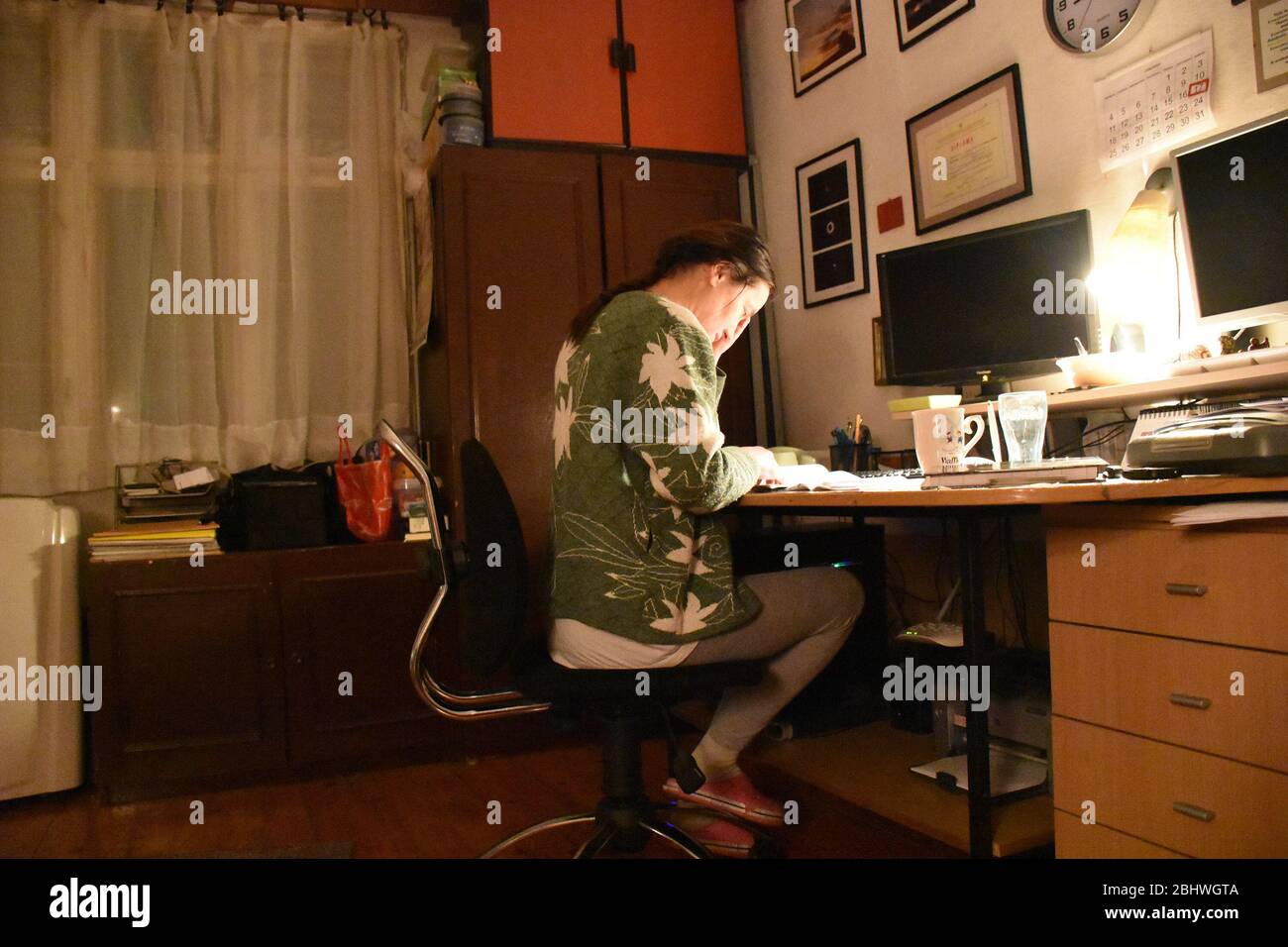 In a desk room in a green colorful sweater sits a girl with long hair ...