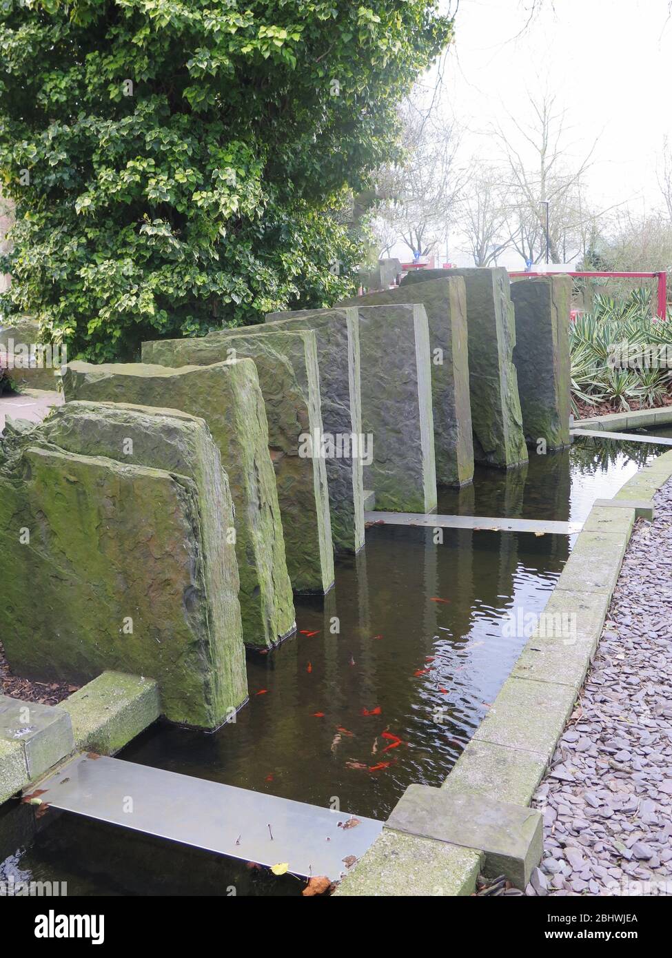 Row of rough hewn rock slabs along small koy pond in public grounds ...