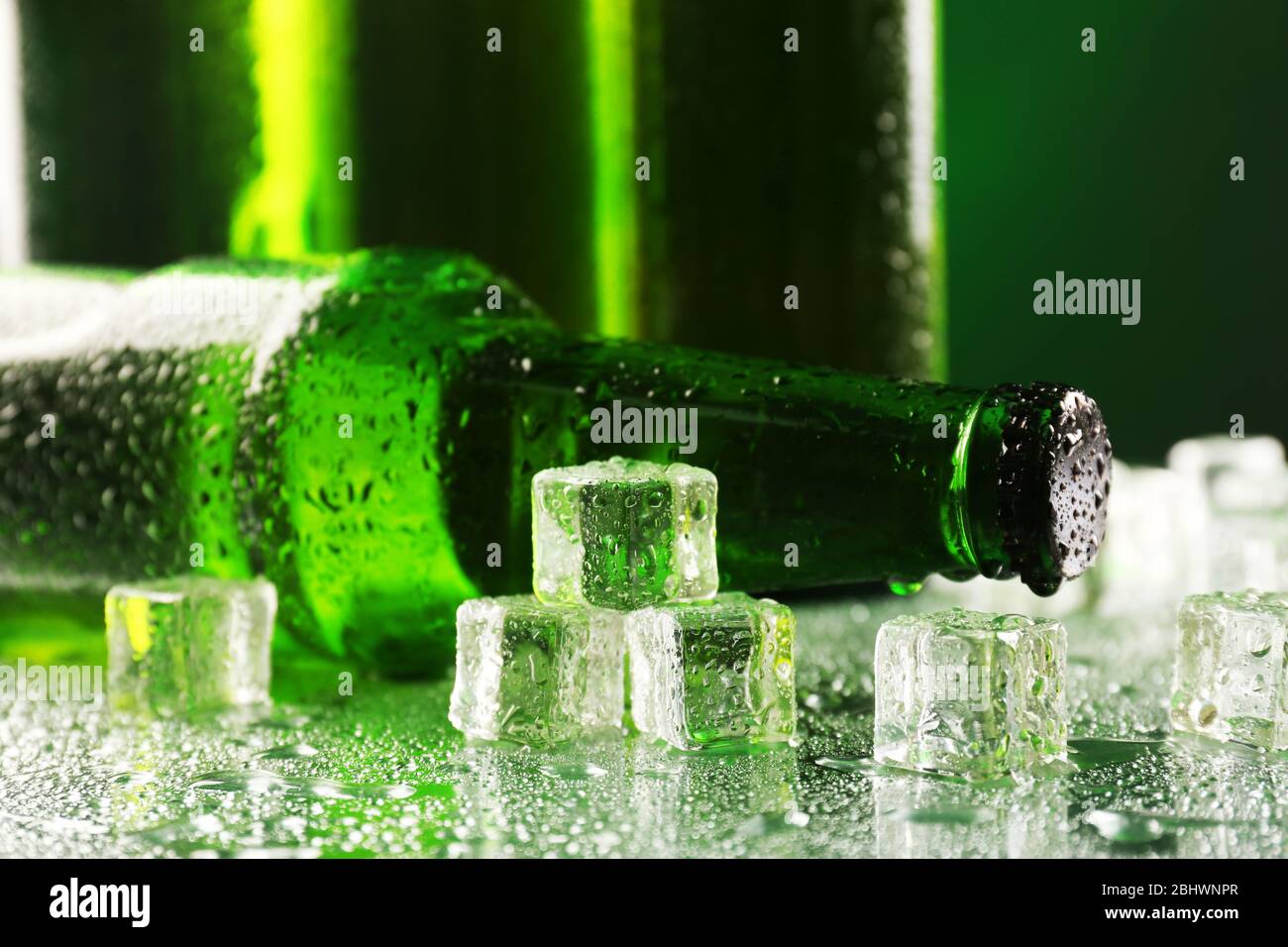 Glass bottles of beer with ice cubes on wet table on dark background ...
