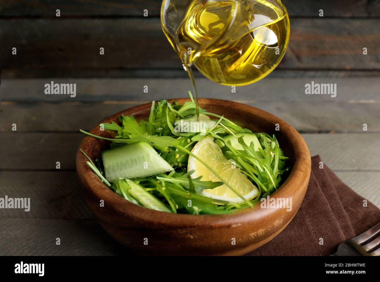 Poring green salad with olive oil on wooden table, closeup Stock Photo ...