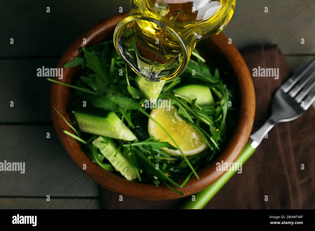 Poring green salad with olive oil on wooden table, closeup Stock Photo ...