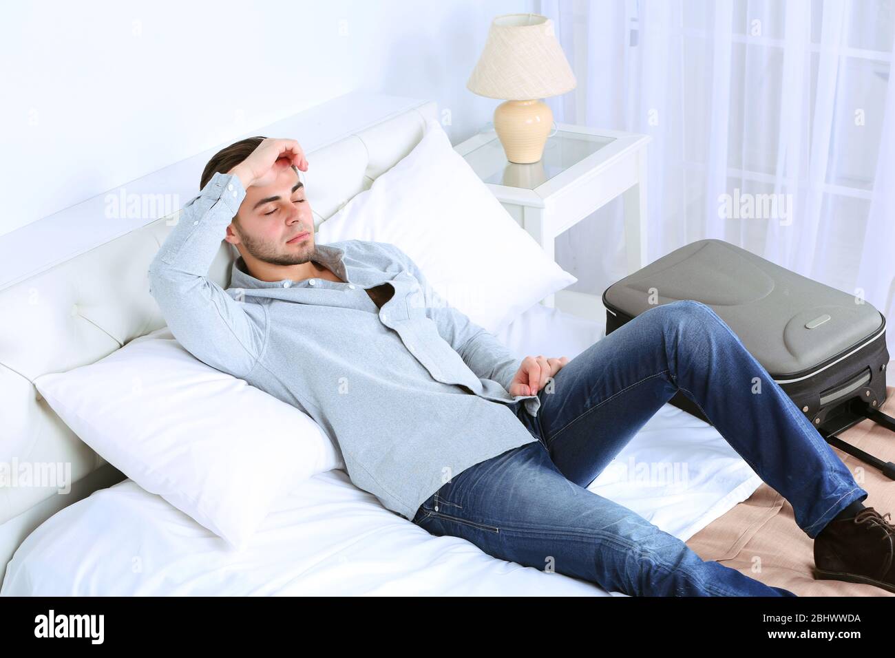 Tired man resting on bed in room Stock Photo - Alamy