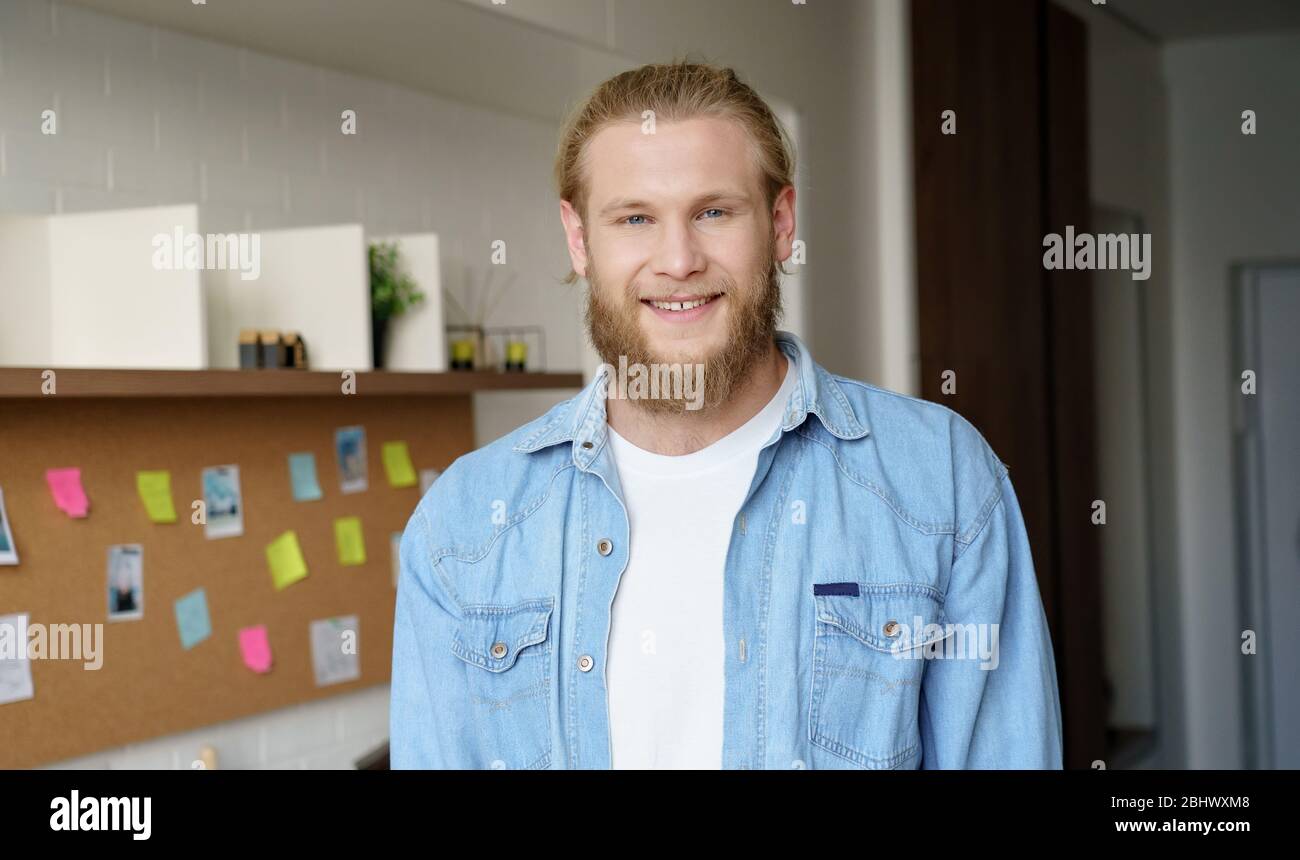 Positive young hipster man standing at home office looking at camera ...