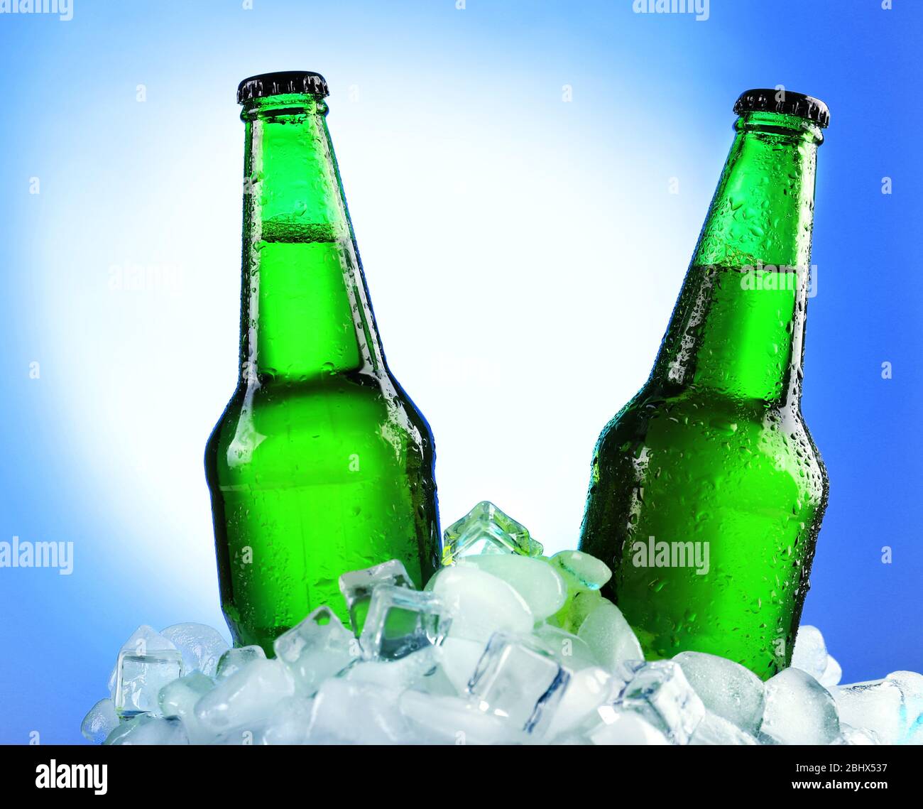 Glass bottles of beer in ice cubes on color background Stock Photo - Alamy