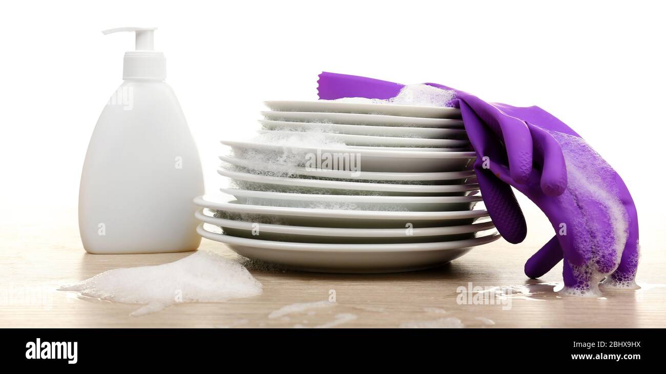 Plates in foam with gloves and cleanser on table isolated on white ...