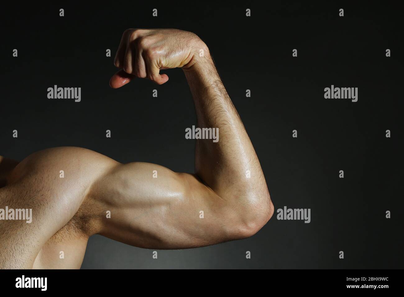 Muscular arm flexing on dark background Stock Photo - Alamy