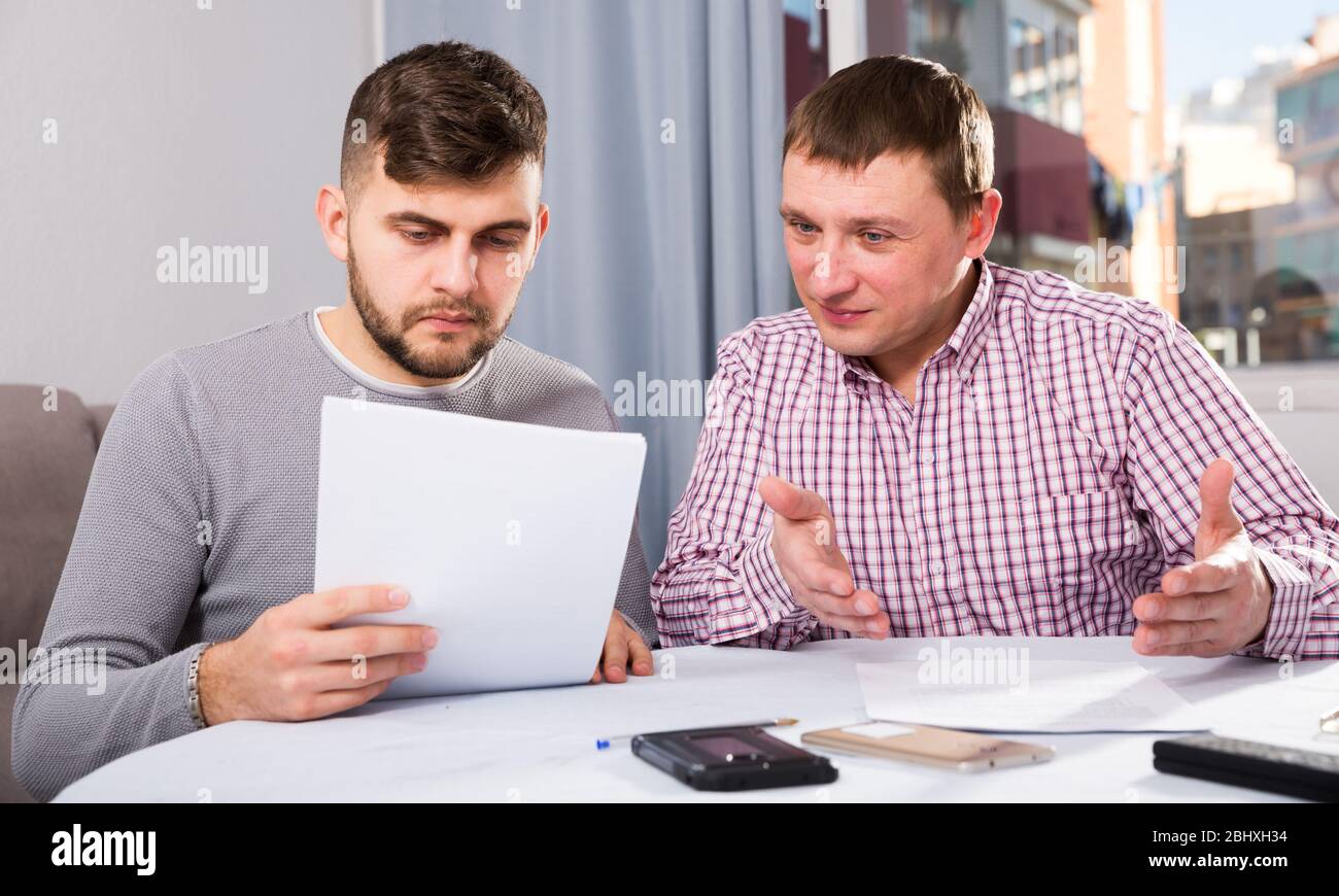 Two serious male friends reading attentively and discussing documents ...