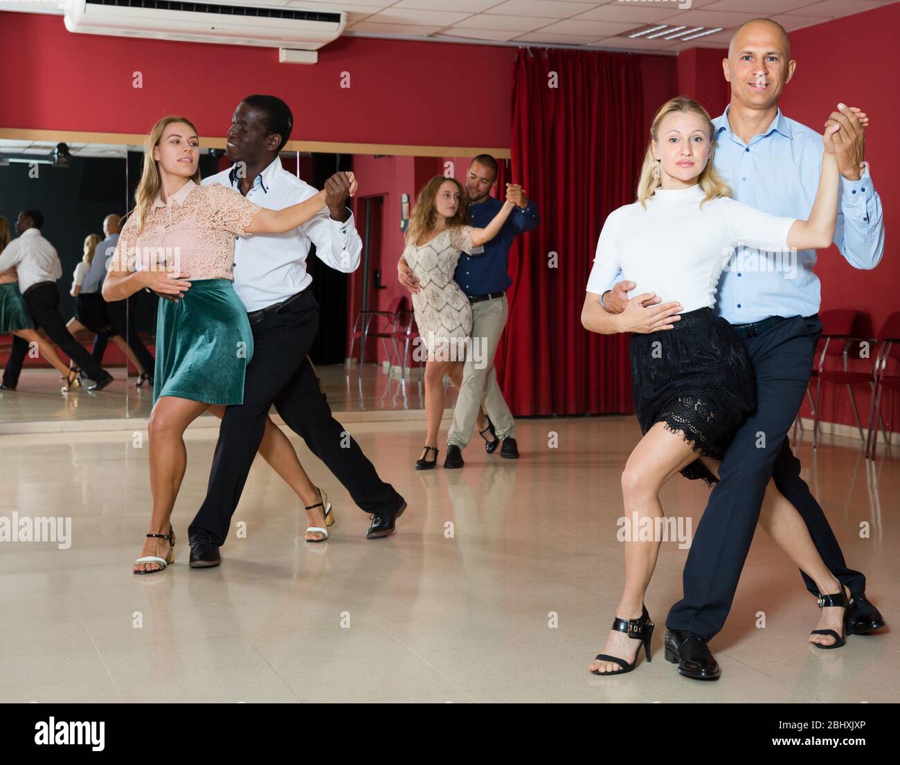 Positive adult couples dancing salsa dance together in modern studio ...
