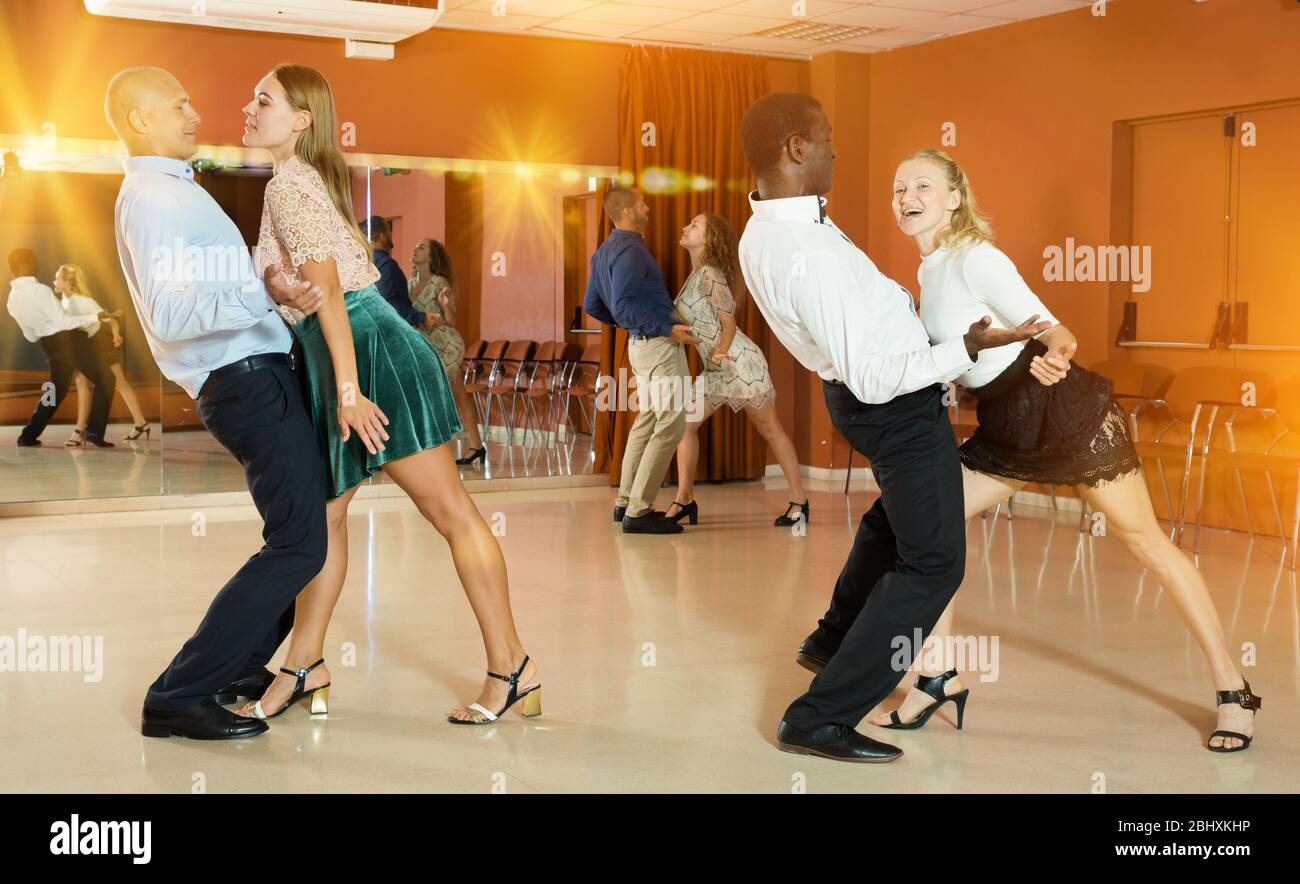 Adult dancing couples enjoying active boogie-woogie in modern studio ...