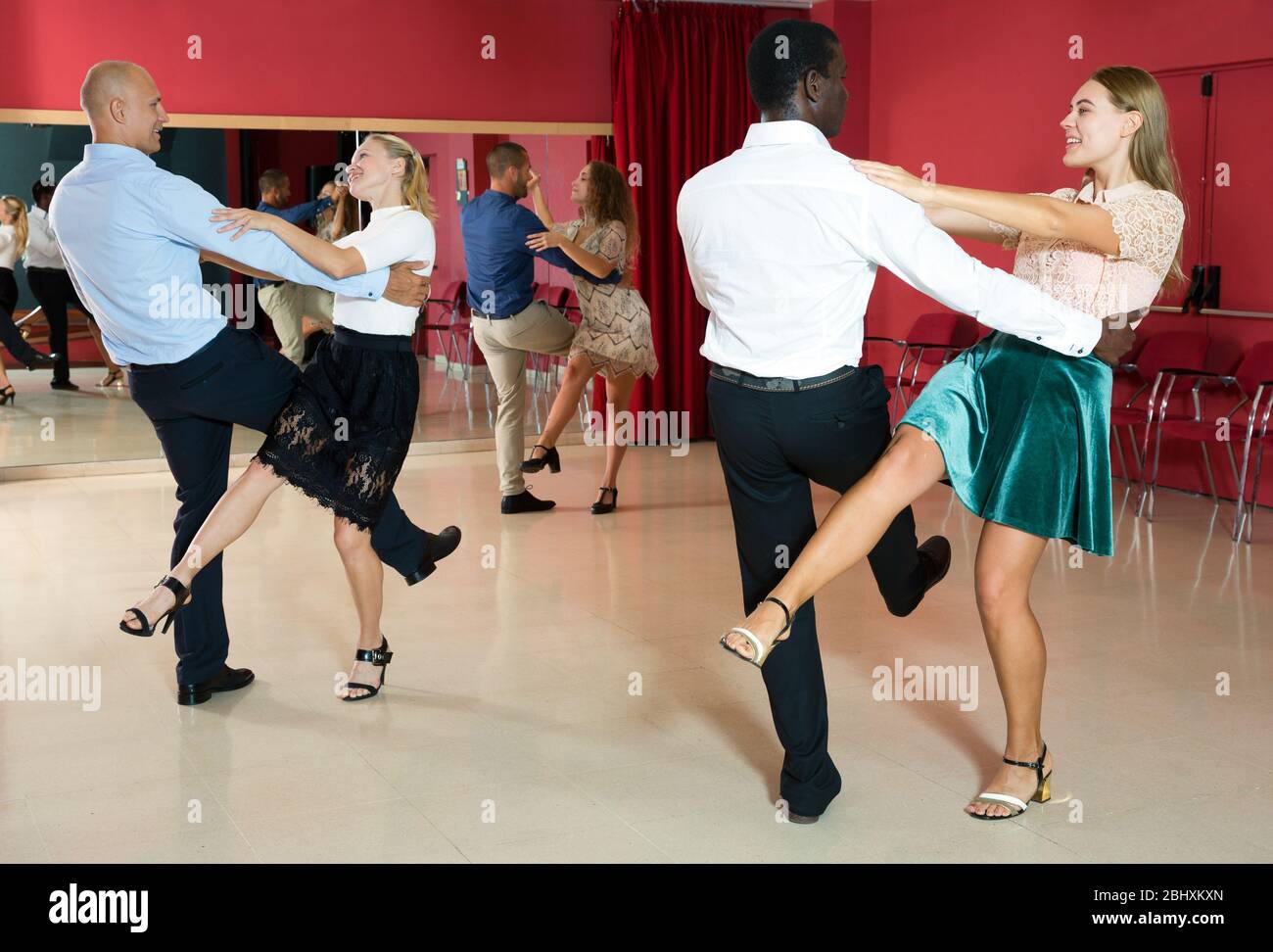 Pairs of young positive people dancing vigorous jive movements in dance ...
