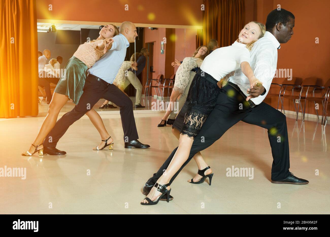 Positive adult couples dancing active dance together in modern studio ...