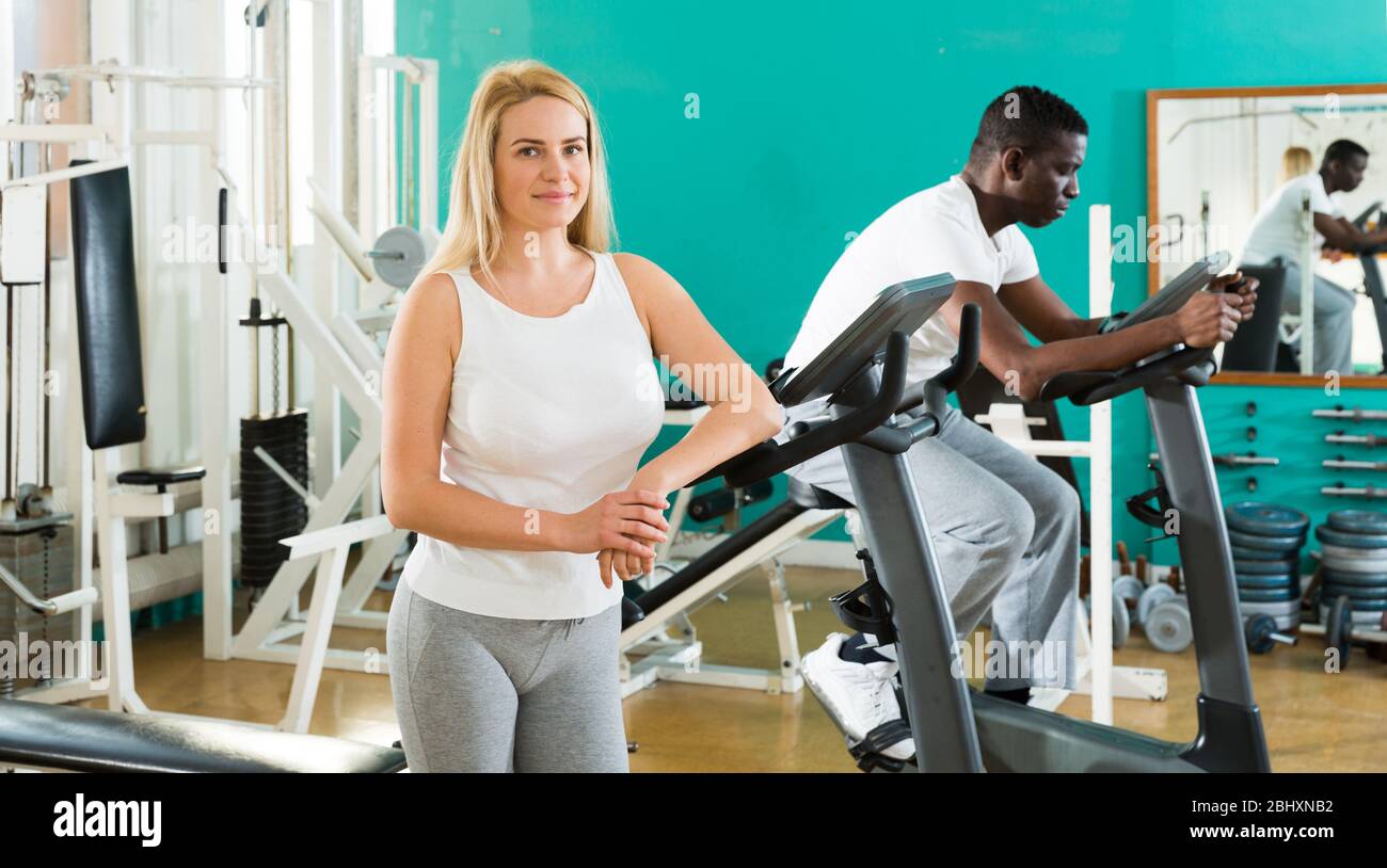 Portrait of positive friendly girl welcoming to gym with exercising man ...