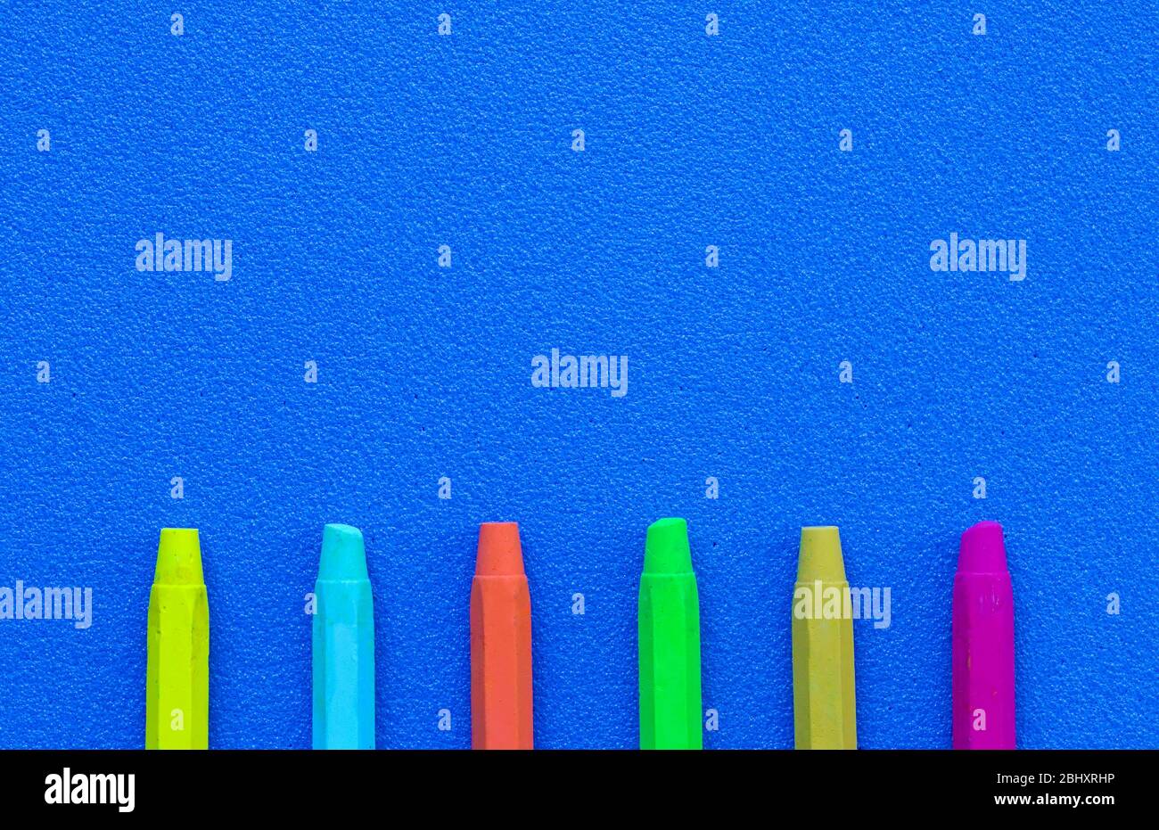 Multi-colored crayons on blue board. Top view. Copy space. Early ...