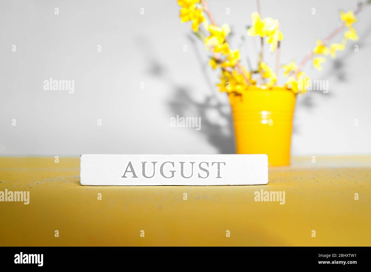 lettering August on a piece of wood with yellow small metal bucket for ...