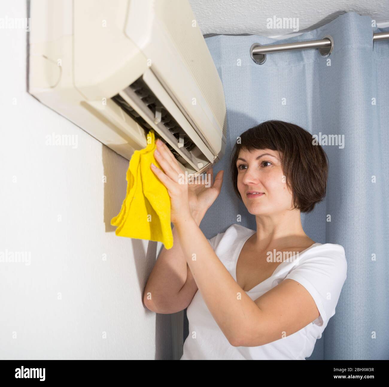Positive woman dusting with rag air conditioning device at her home ...