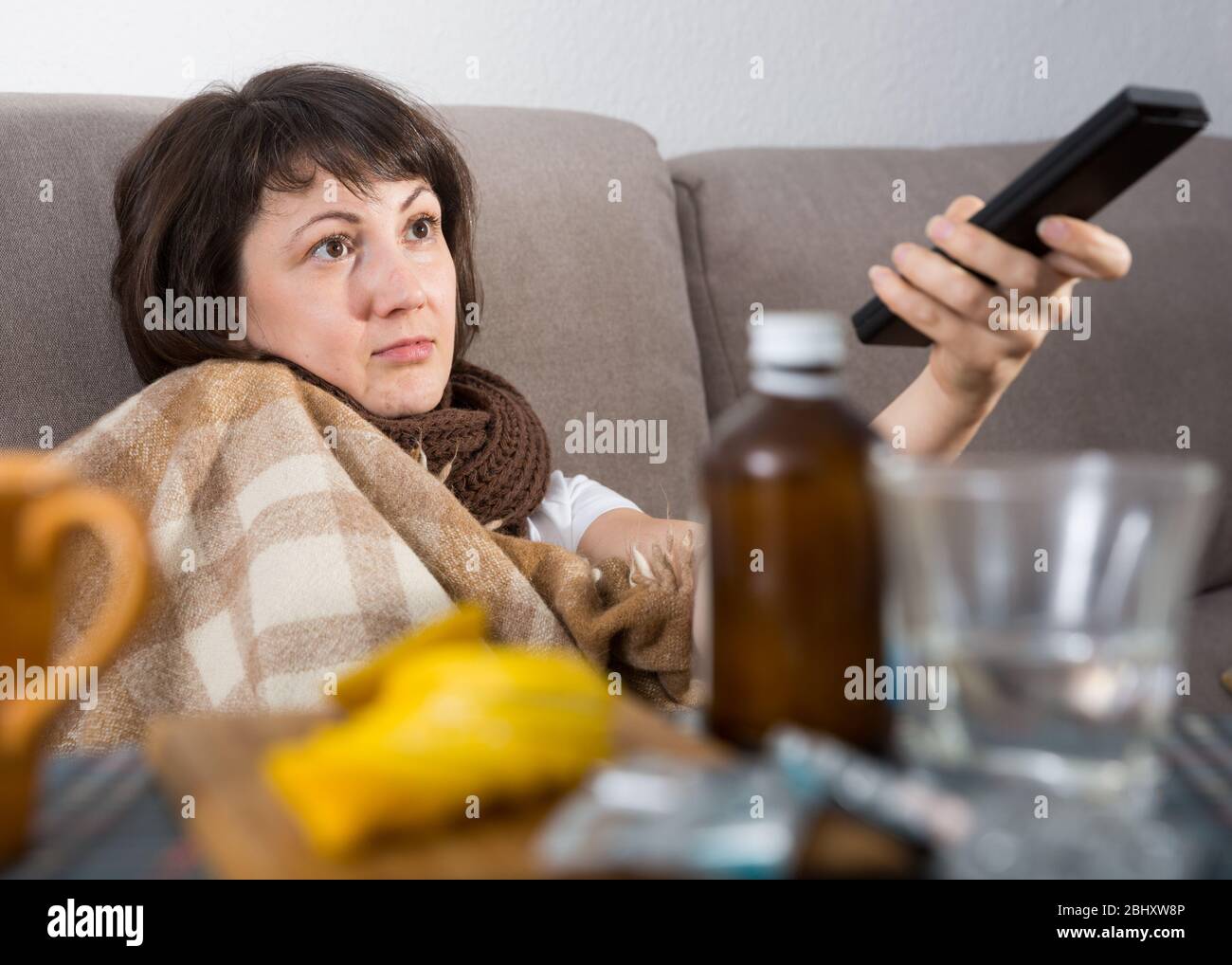 Sick woman wrapped in blanket holding TV remote control at home Stock ... Sick woman wrapped in blanket holding TV remote control at home Stock ...