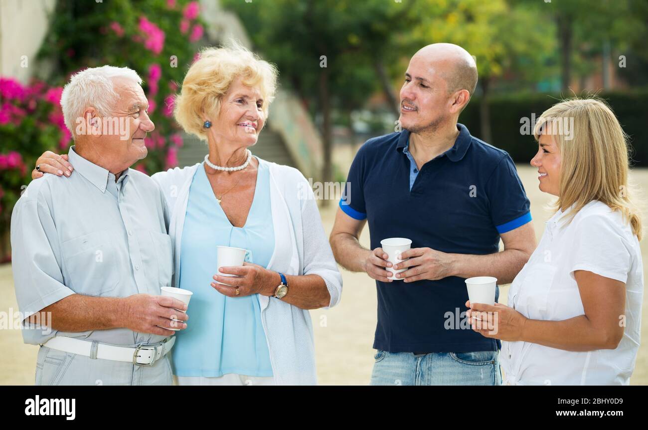 Happy aged parents with his adult children drink water and talk in the ...