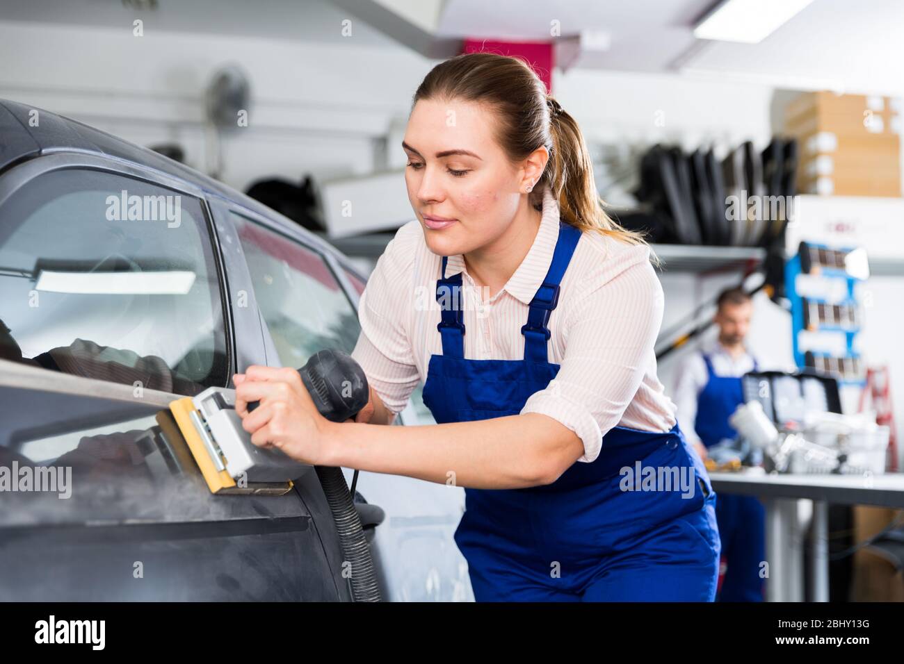 Young woman car mechanic in workshop sanding automobile body, preparing ...