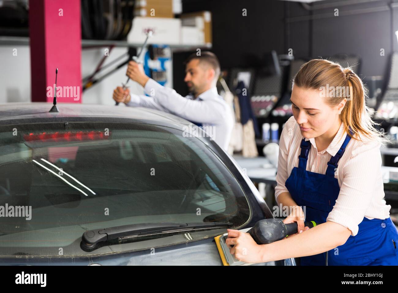 Young woman car mechanic in workshop sanding automobile body, preparing ...