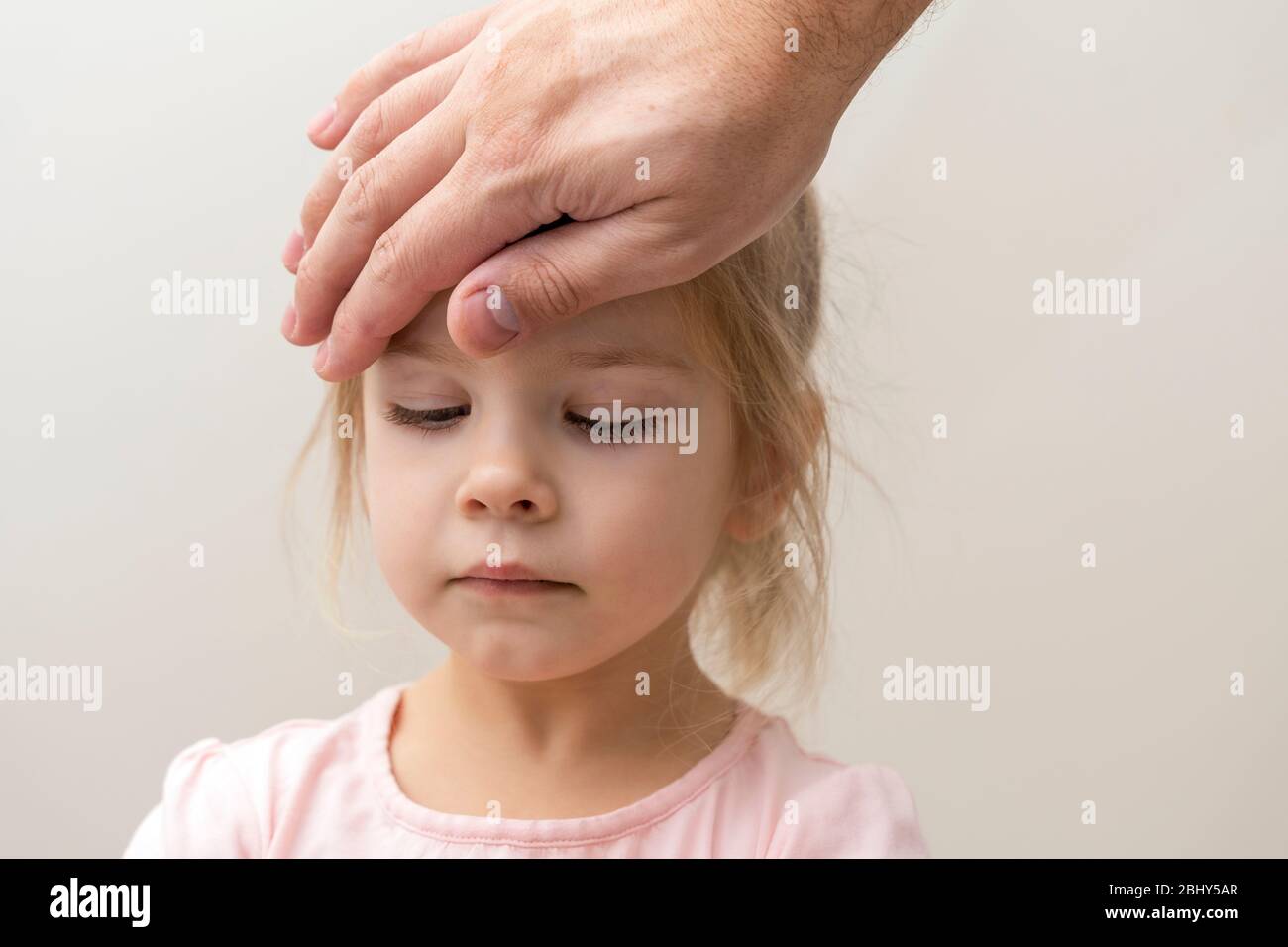 the man’s hand lies on the forehead of a three-year-old girl. Dad ...