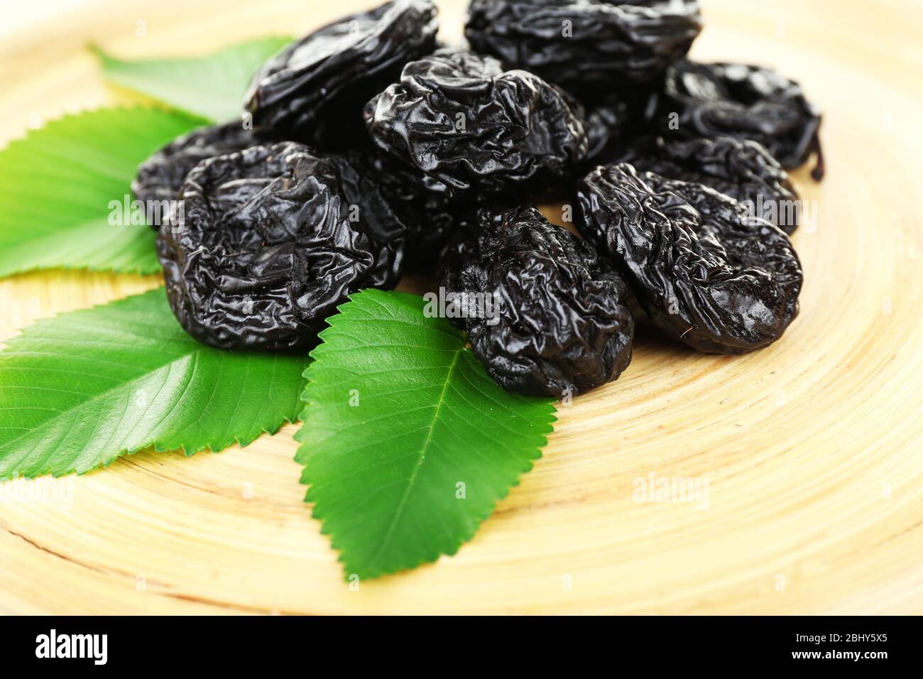 Pile of prunes with leaves on wooden tray, closeup Stock Photo - Alamy