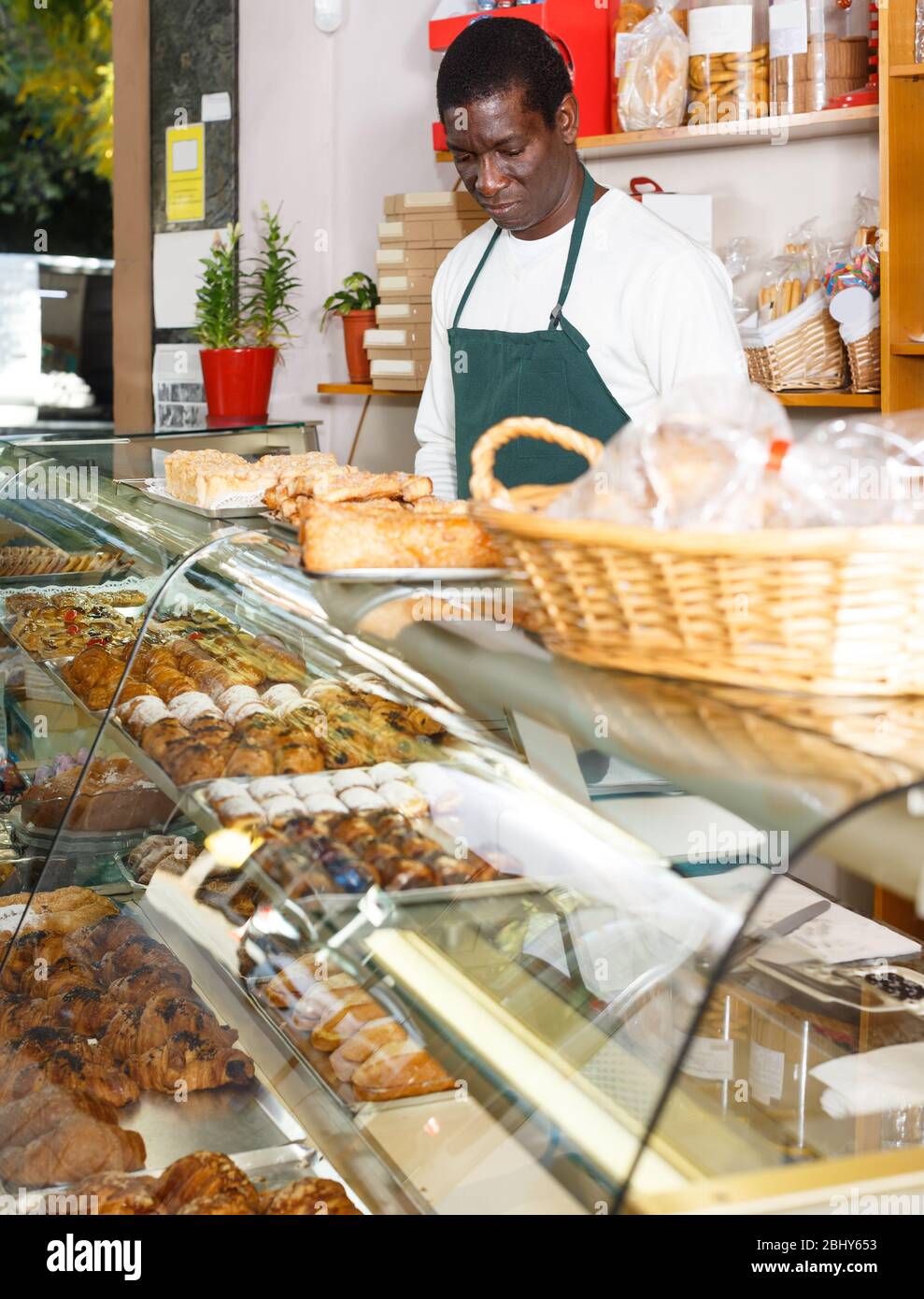 Skillful African American baker working in small bakery, arranging ...