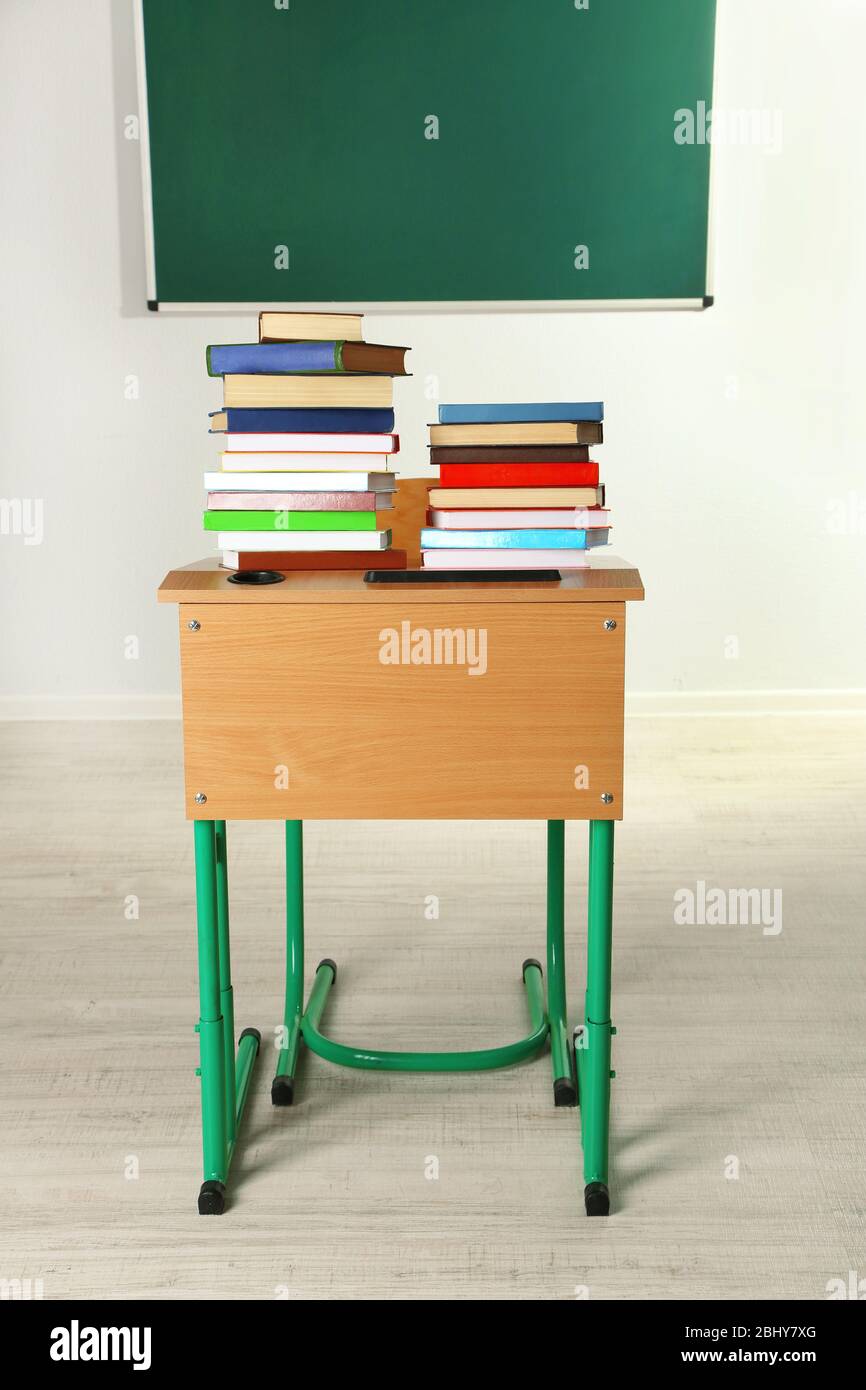 Wooden desk with books and chair in class on blackboard background ...