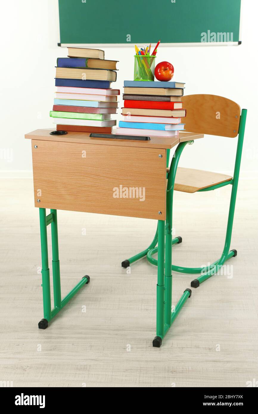 Wooden desk with books and chair in class on blackboard background ...