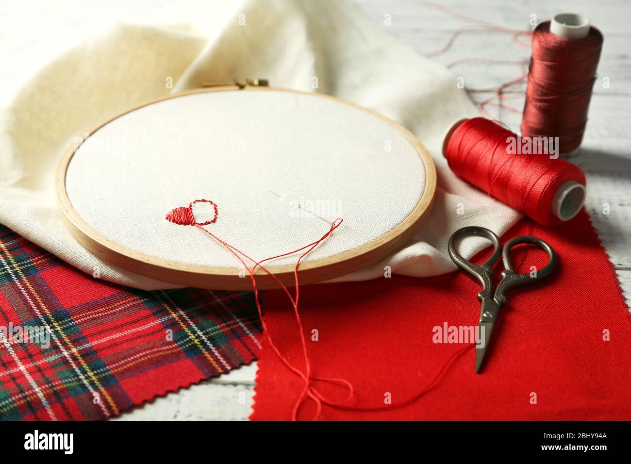 The embroidery hoop with canvas and red sewing threads on table close ...