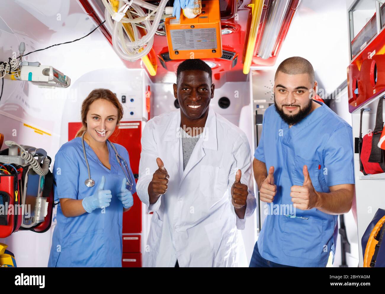 Three positive friendly smiling ambulance doctors posing in ambulance ...
