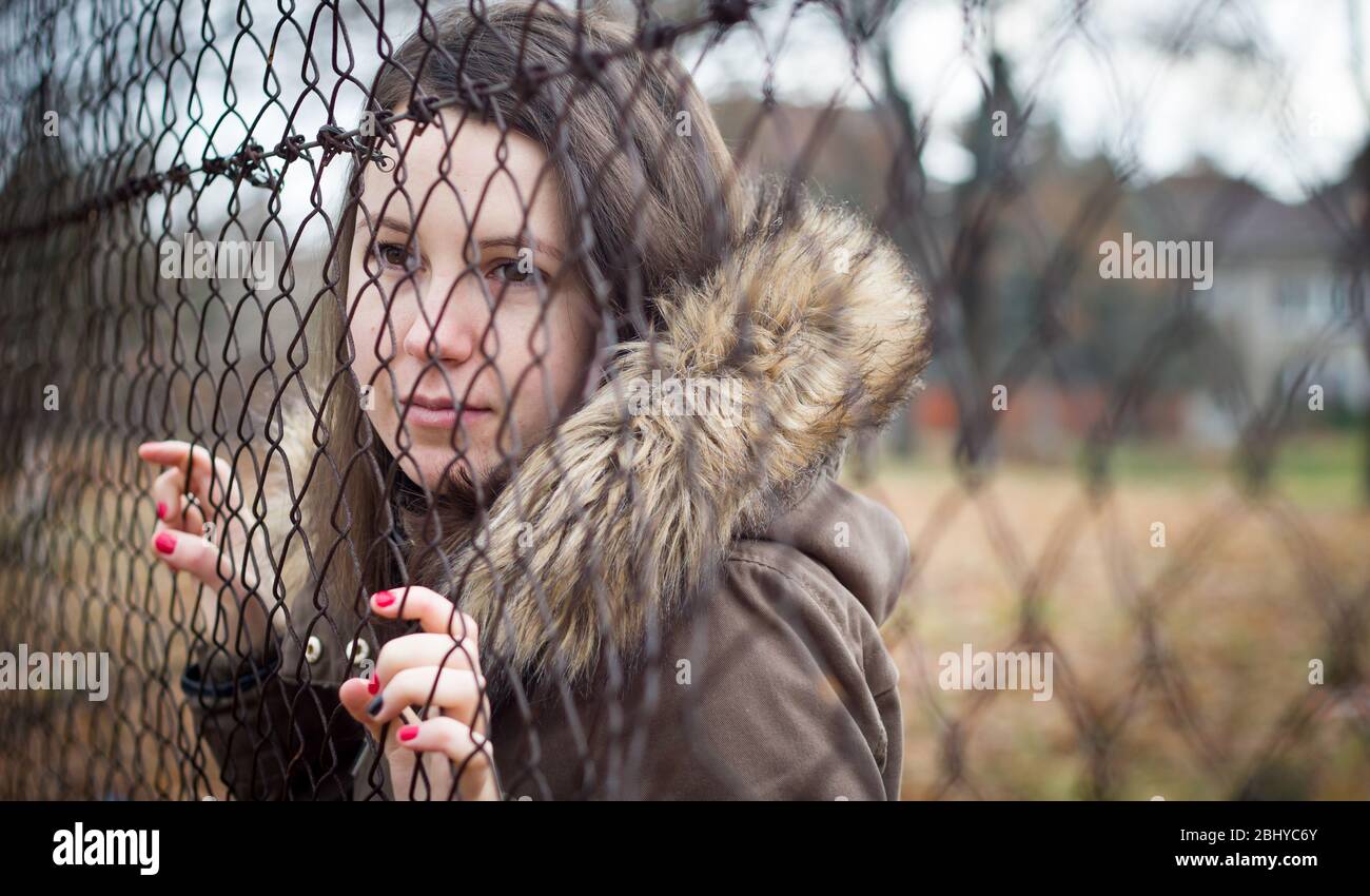 Pretty young girl holding the fence, looking sad, depressed mood ...