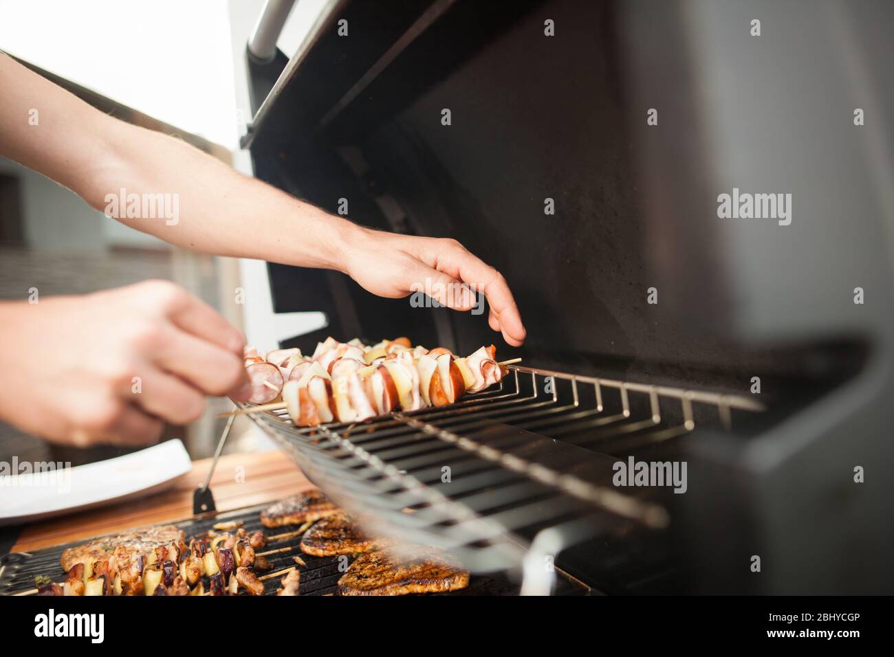 Hand of young man grilling some meat and vegetable-meat skewers on huge ...