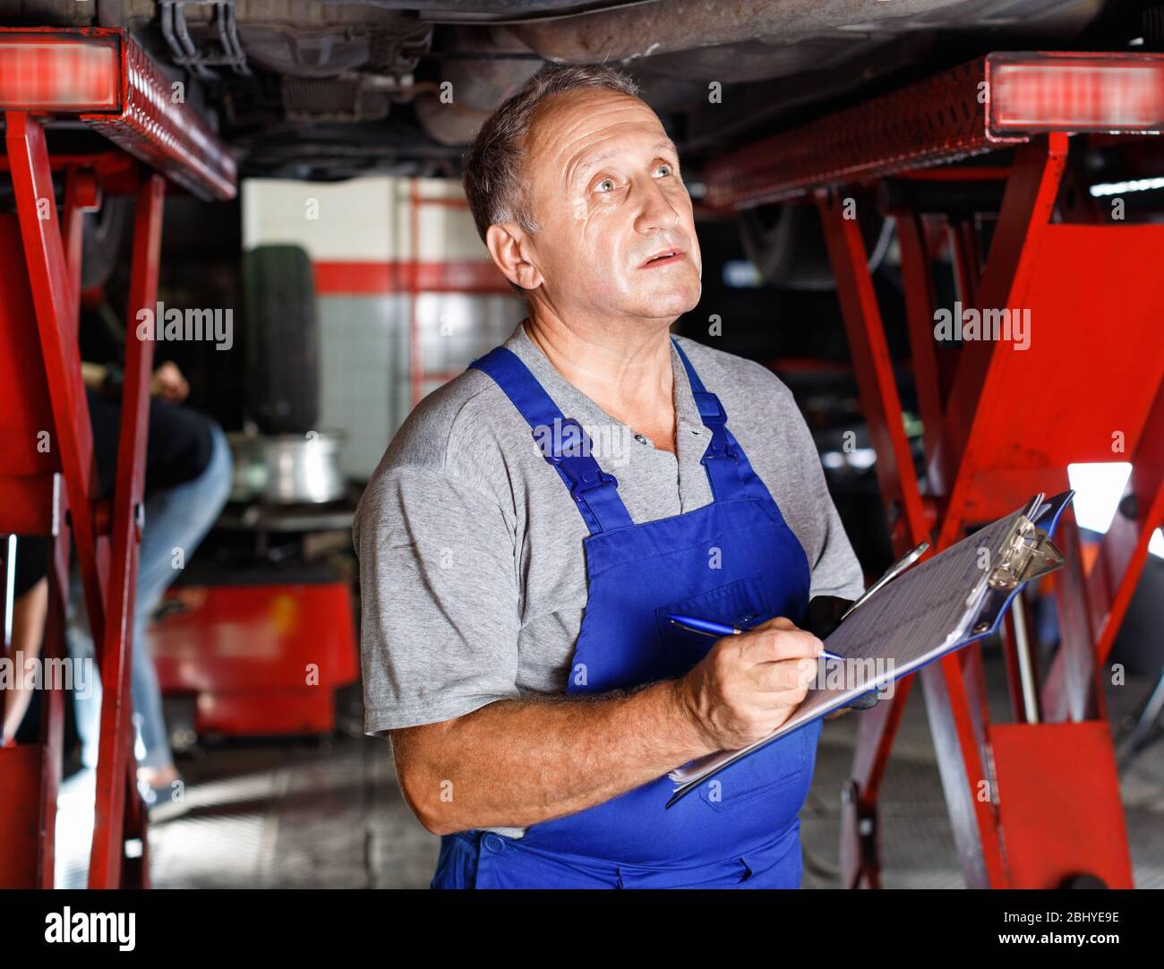 Skilled glad positive smiling mature male mechanic taking notes in ...
