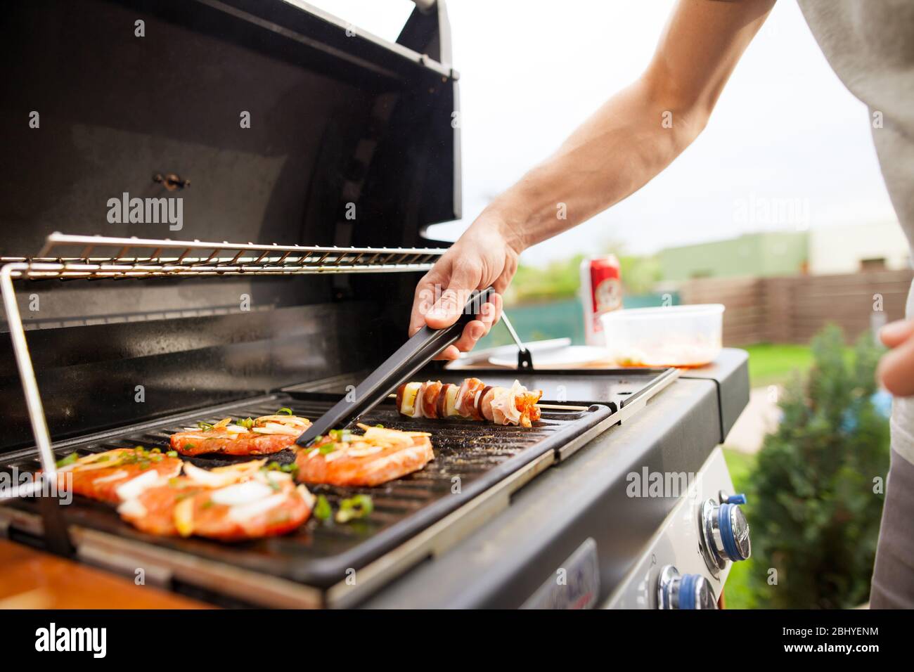 Hand of young man grilling some meat and vegetable-meat skewers on huge ...