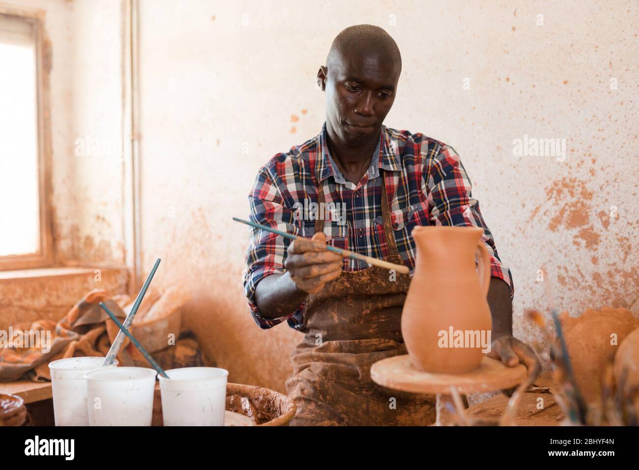 Professional African American male potter painting ceramic pot in ...