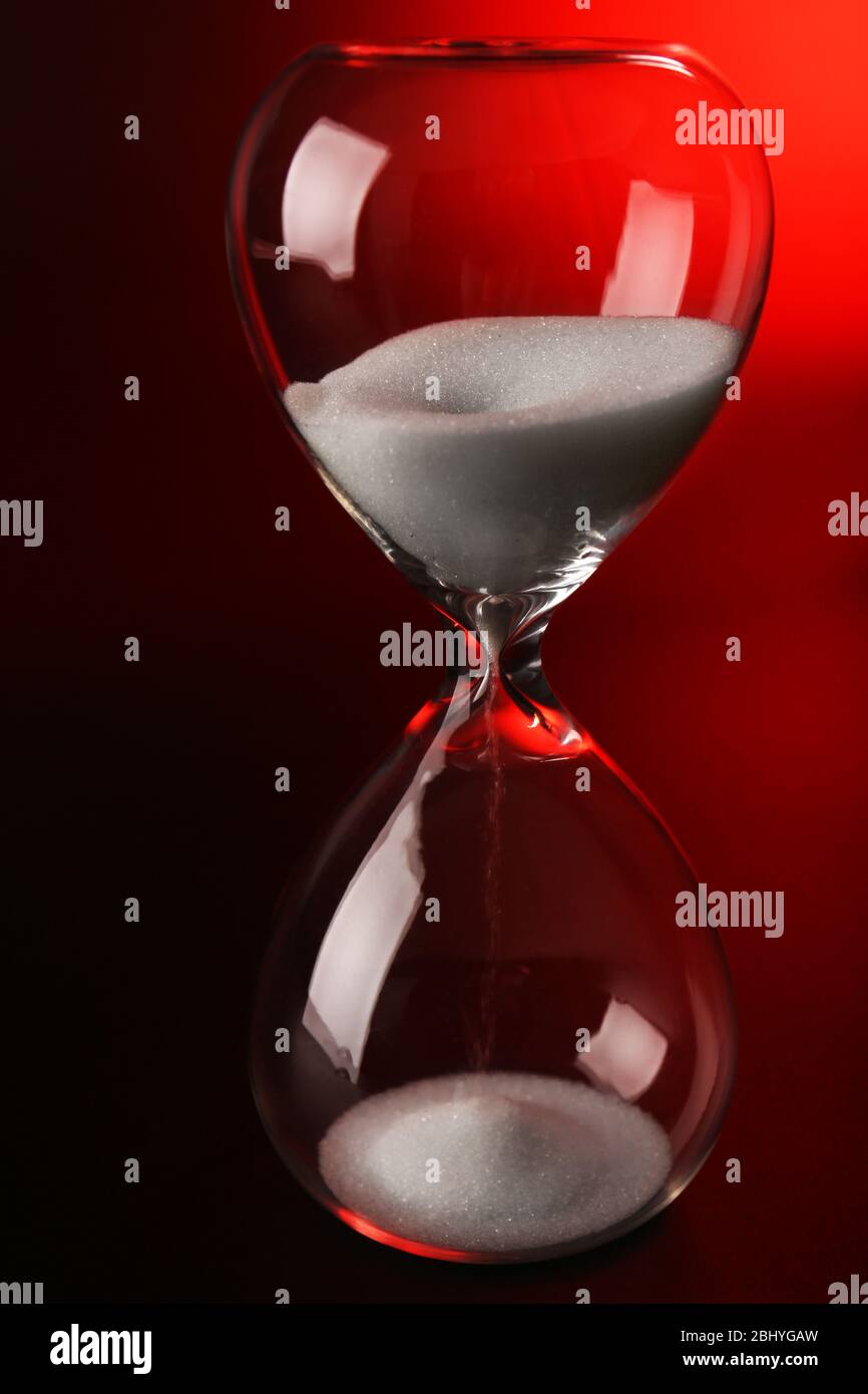 Hourglass on dark red background Stock Photo - Alamy