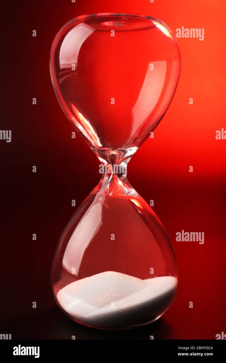 Hourglass on dark red background Stock Photo - Alamy
